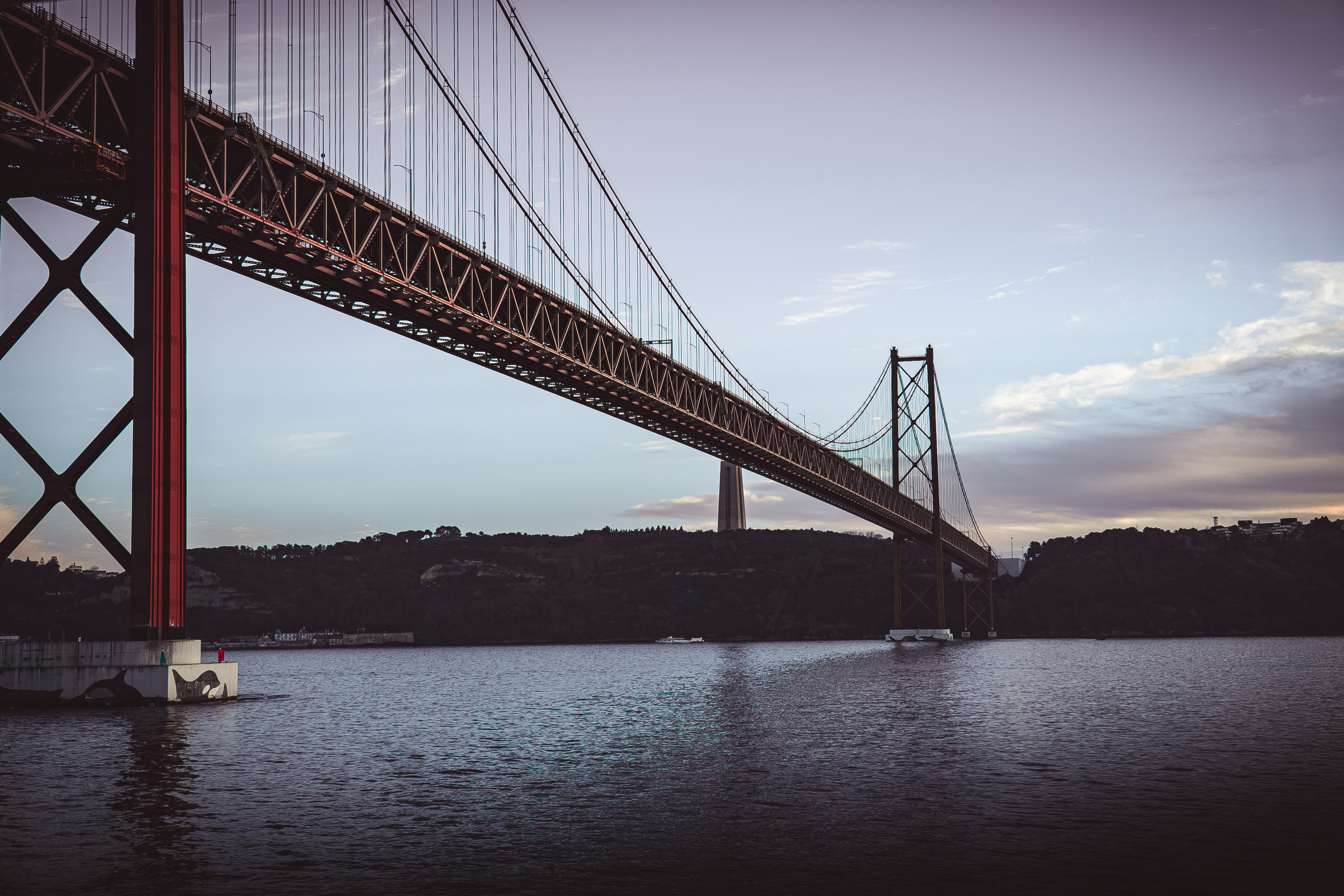25 de Abril Bridge Over the Tagus:A wide evening view of Lisbon’s 25 de Abril Bridge stretching across the Tagus River under a calm blue and purple sky.