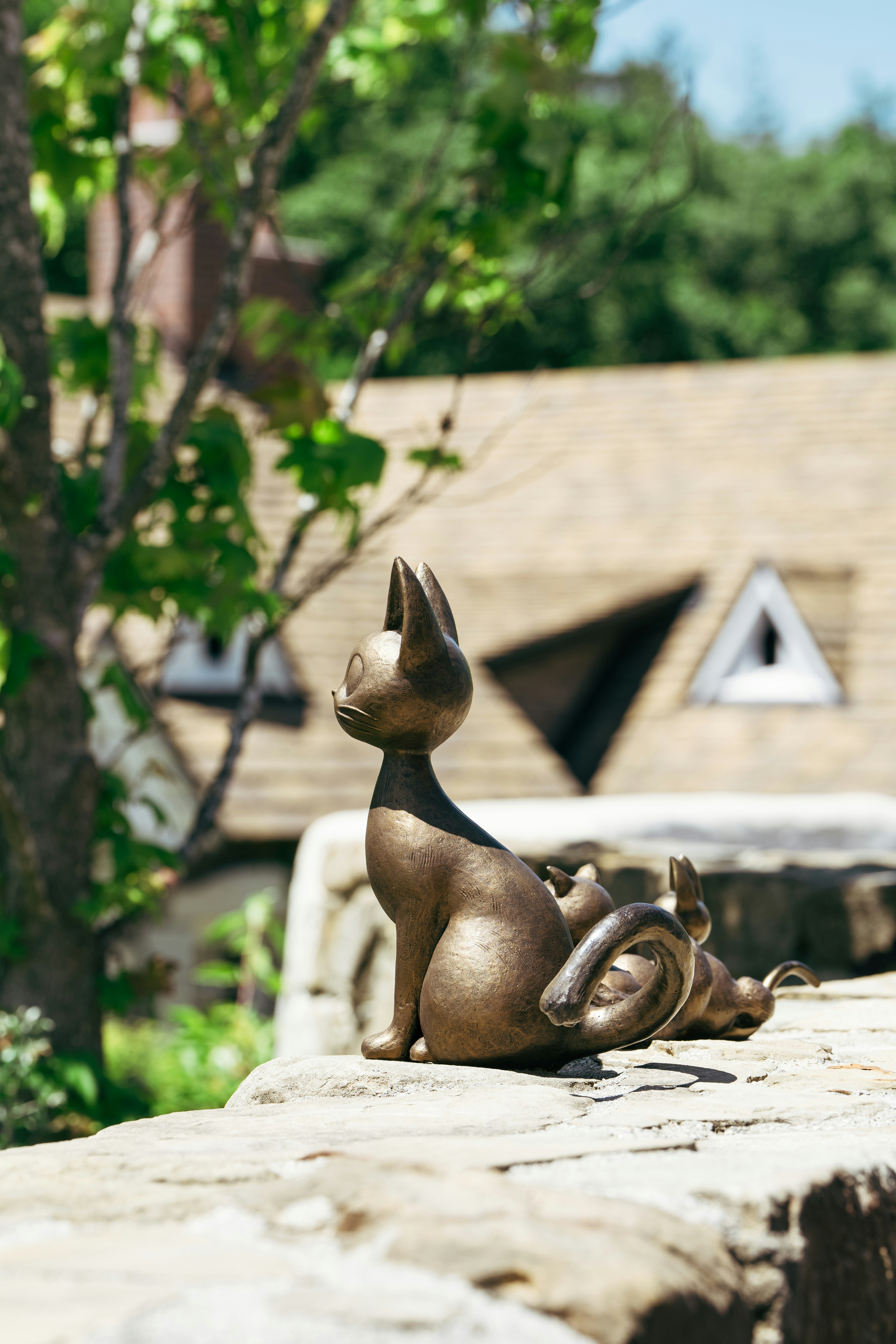 Bronze Cat on the Stone Wall: Tranquil Garden Sculpture in Sunlit Dapple