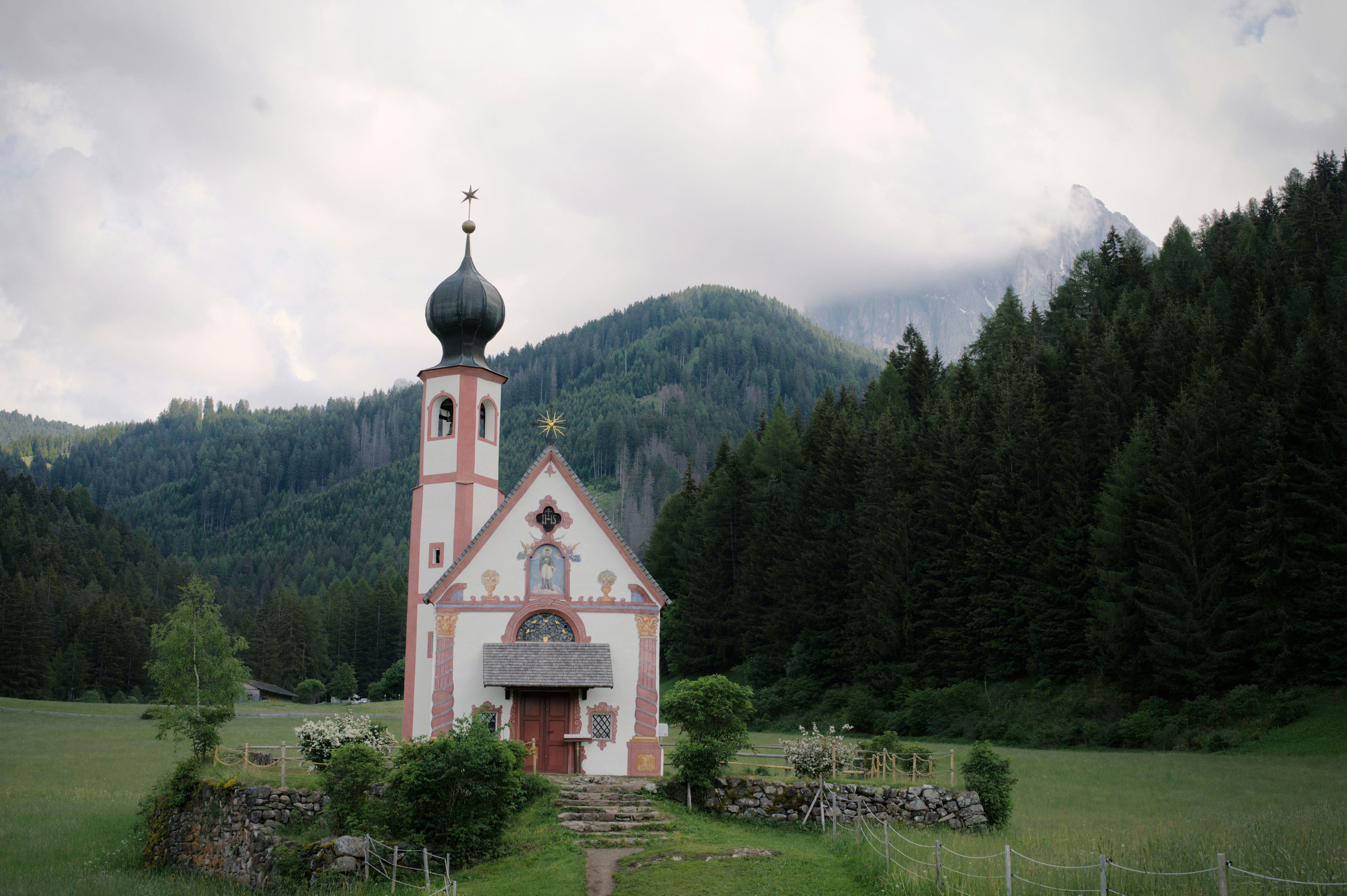 Small chapel in a meadow framed by pines and distant mountains