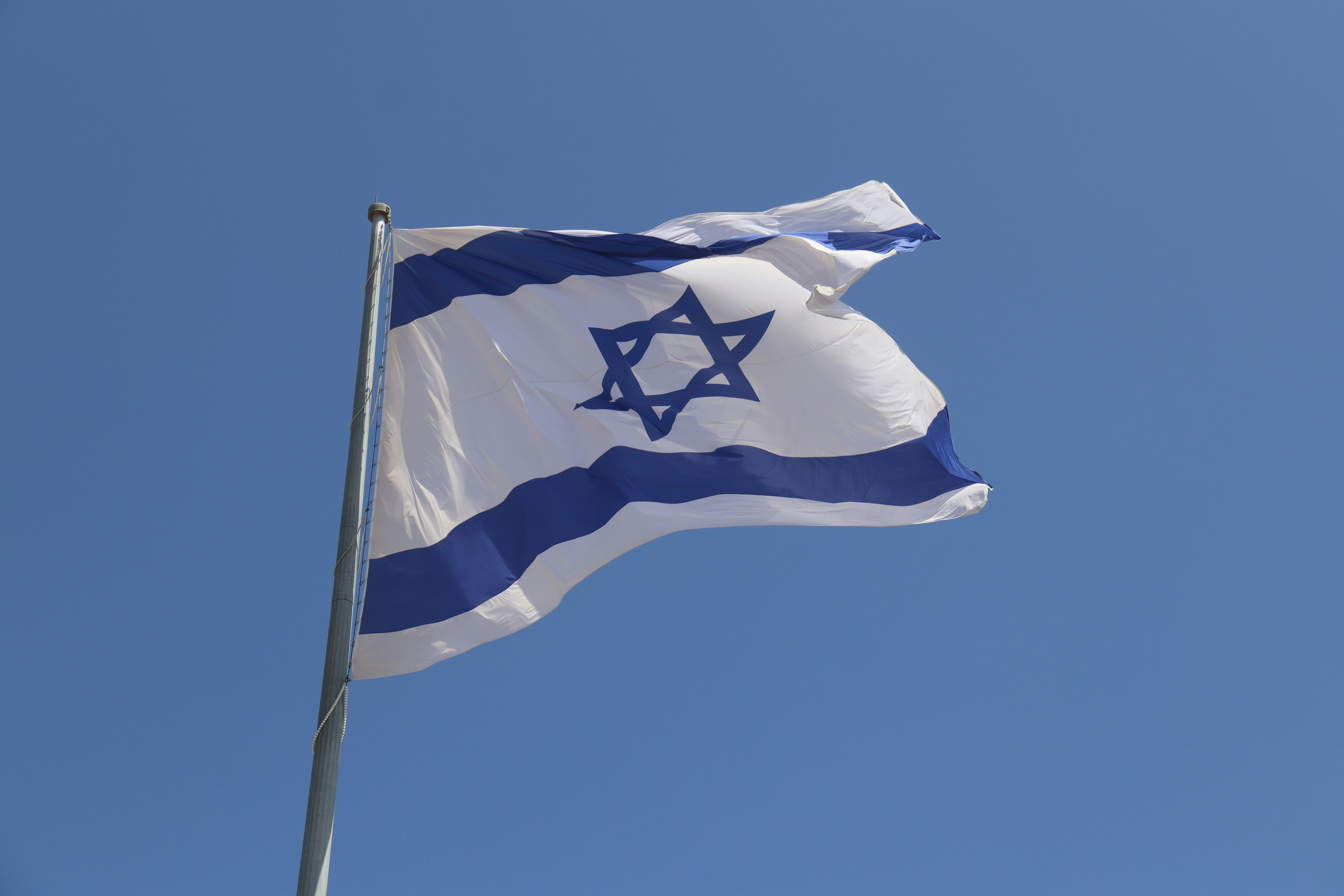 Bright blue flag with the Star of David flies against a crisp blue sky, captured with a clear, uncluttered composition.