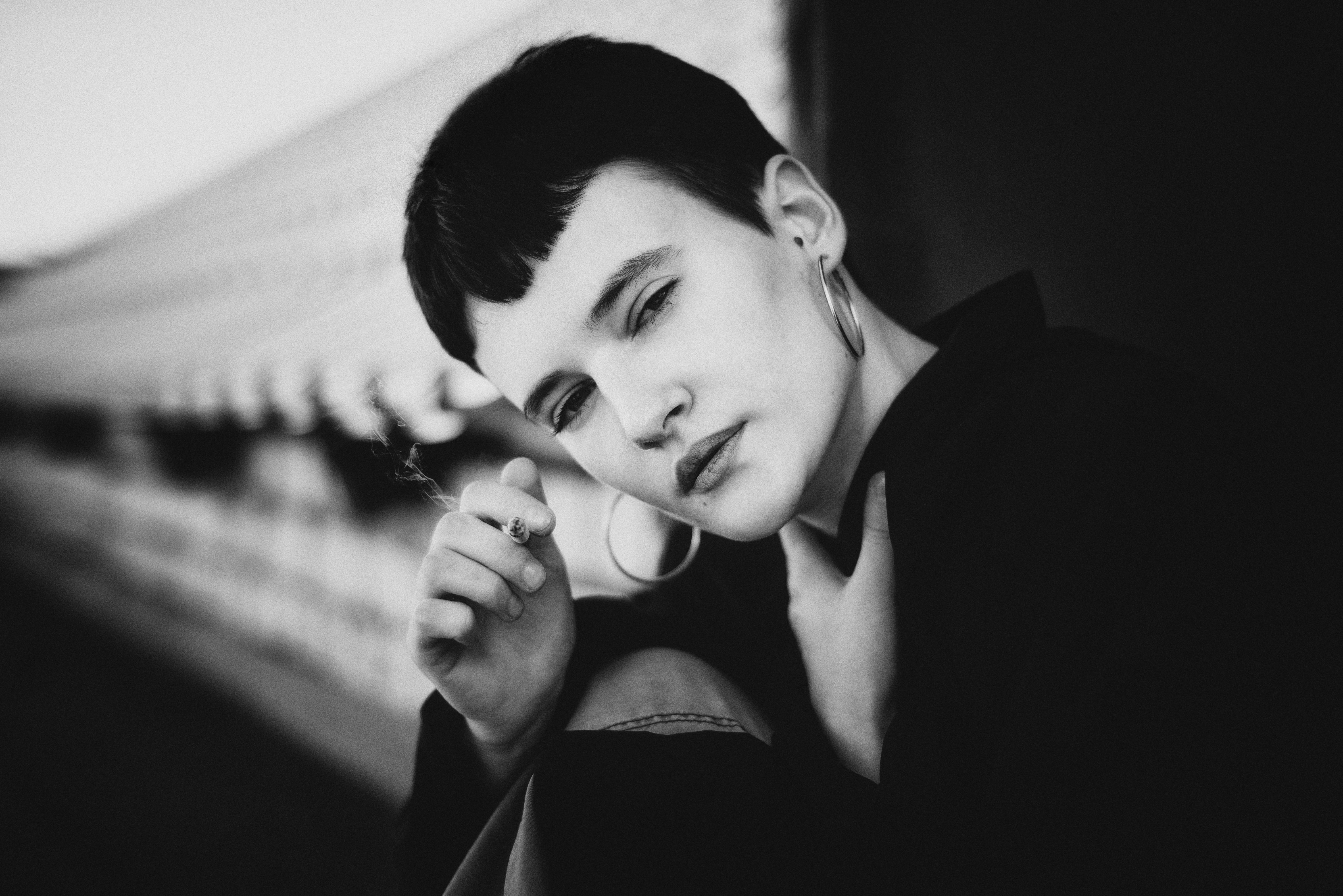 Monochrome portrait emphasizing the subject's intense gaze and bold haircut against a blurred backdrop. A lone figure with hoop earrings conveys mood and attitude; the image reads as a candid, fashion-inspired study.