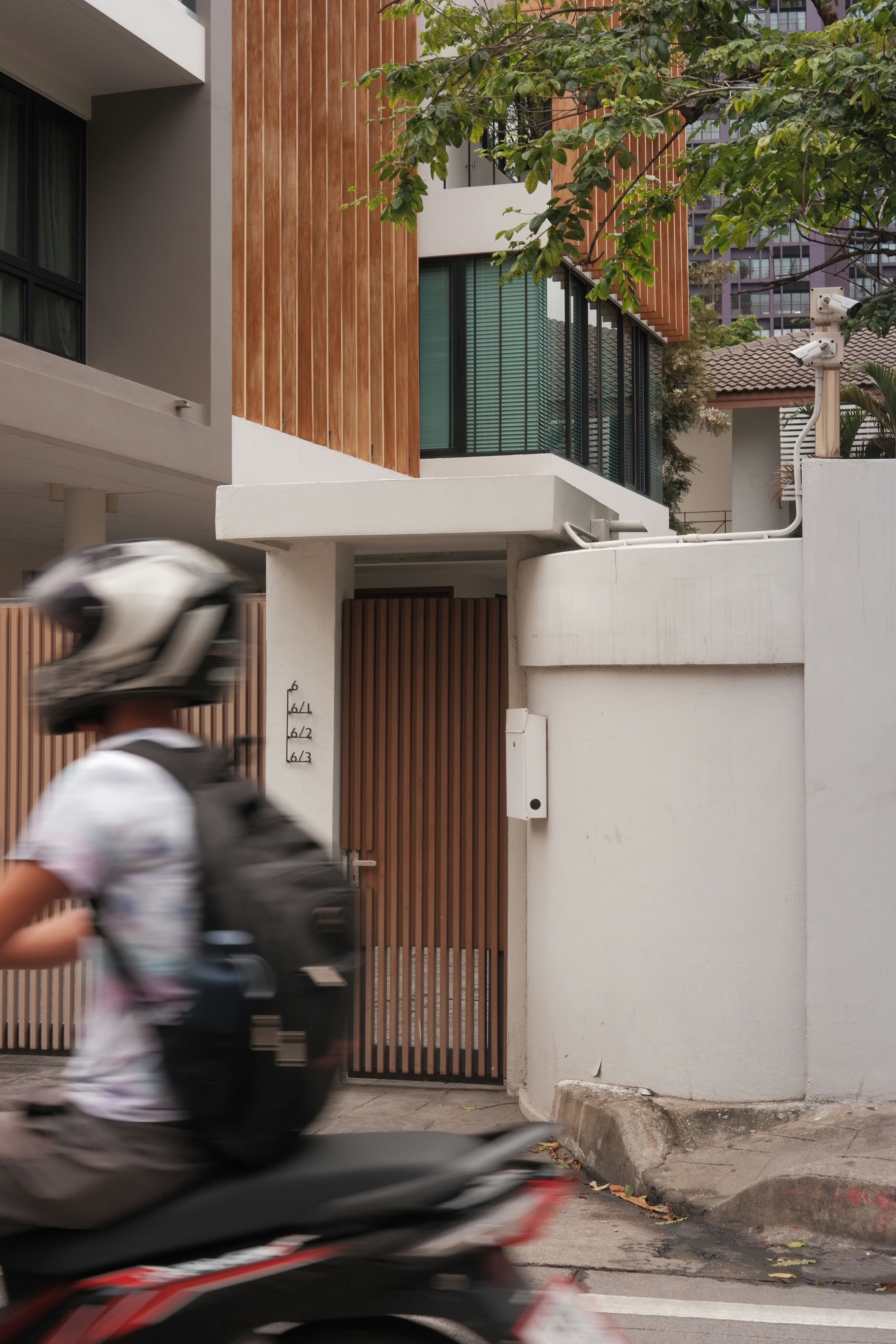 Blurred rider passes by a modern building with wooden slats and white walls, capturing a sense of everyday movement in an urban setting.