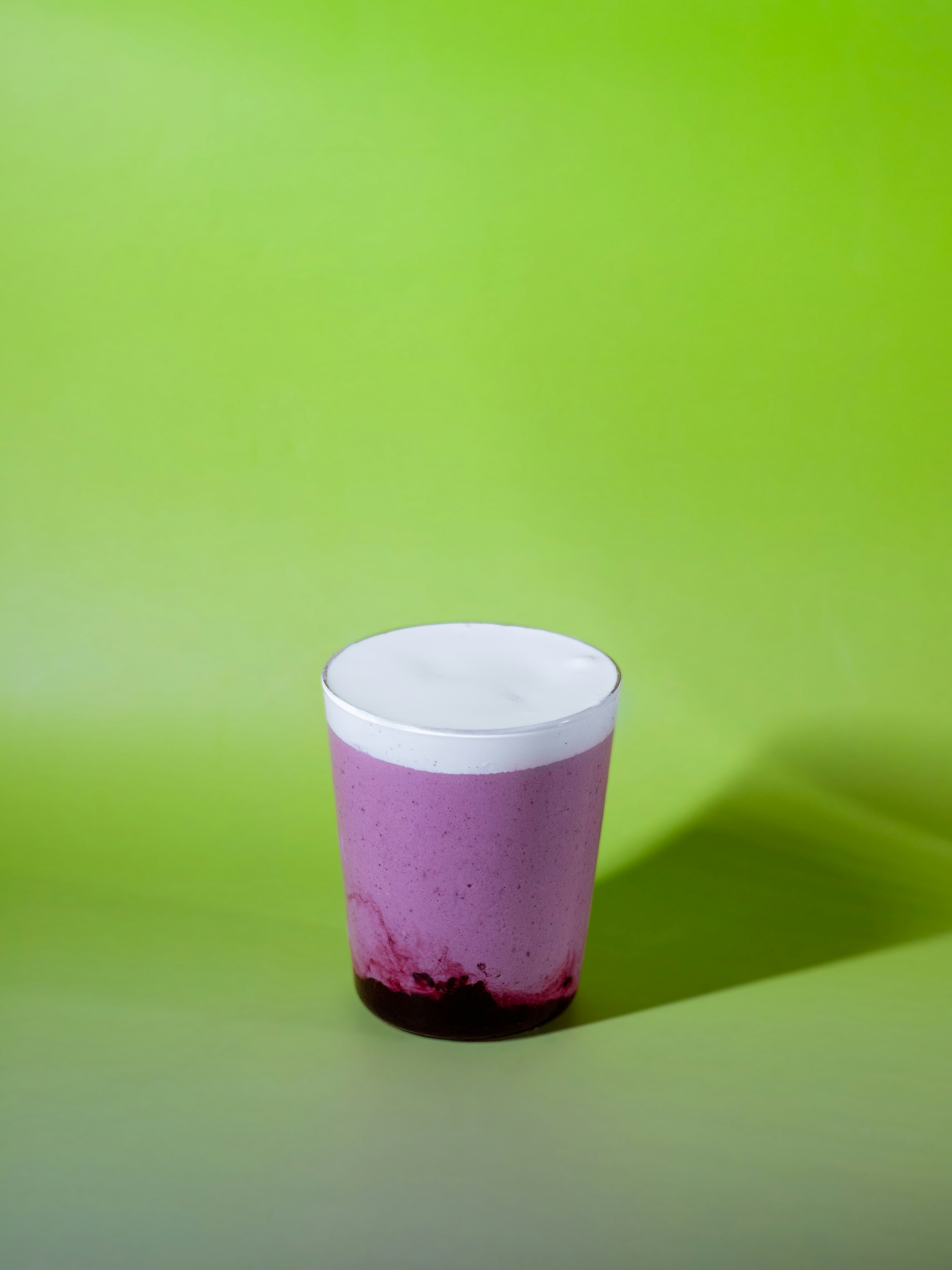 A single purple smoothie cup sits on a lime-green surface with a matching backdrop, creating a minimalist still-life composition.