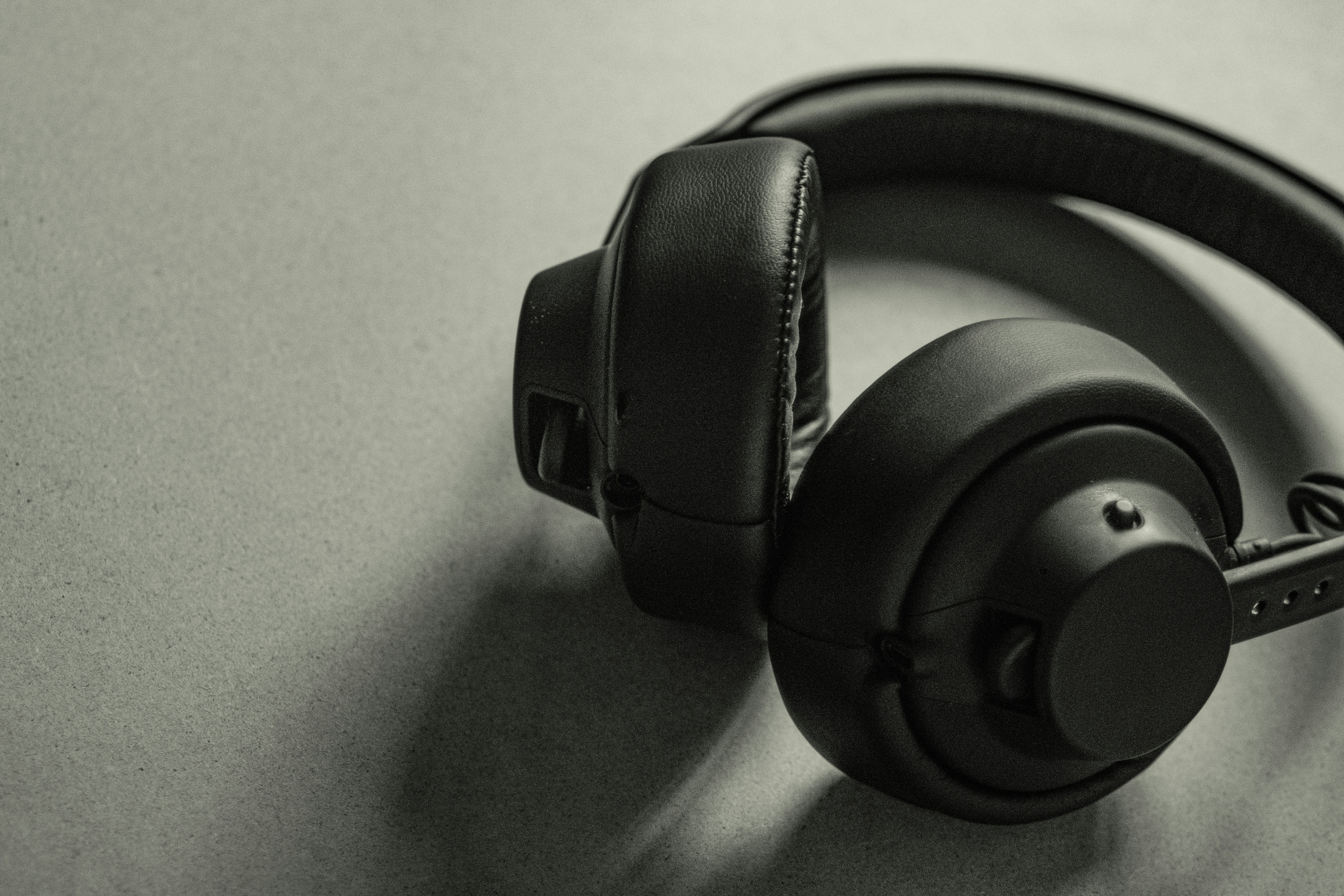 Over-ear headphones lie on a smooth, neutral surface, captured with soft lighting and muted tones to emphasize texture and form. This is a product/studio-style presentation.