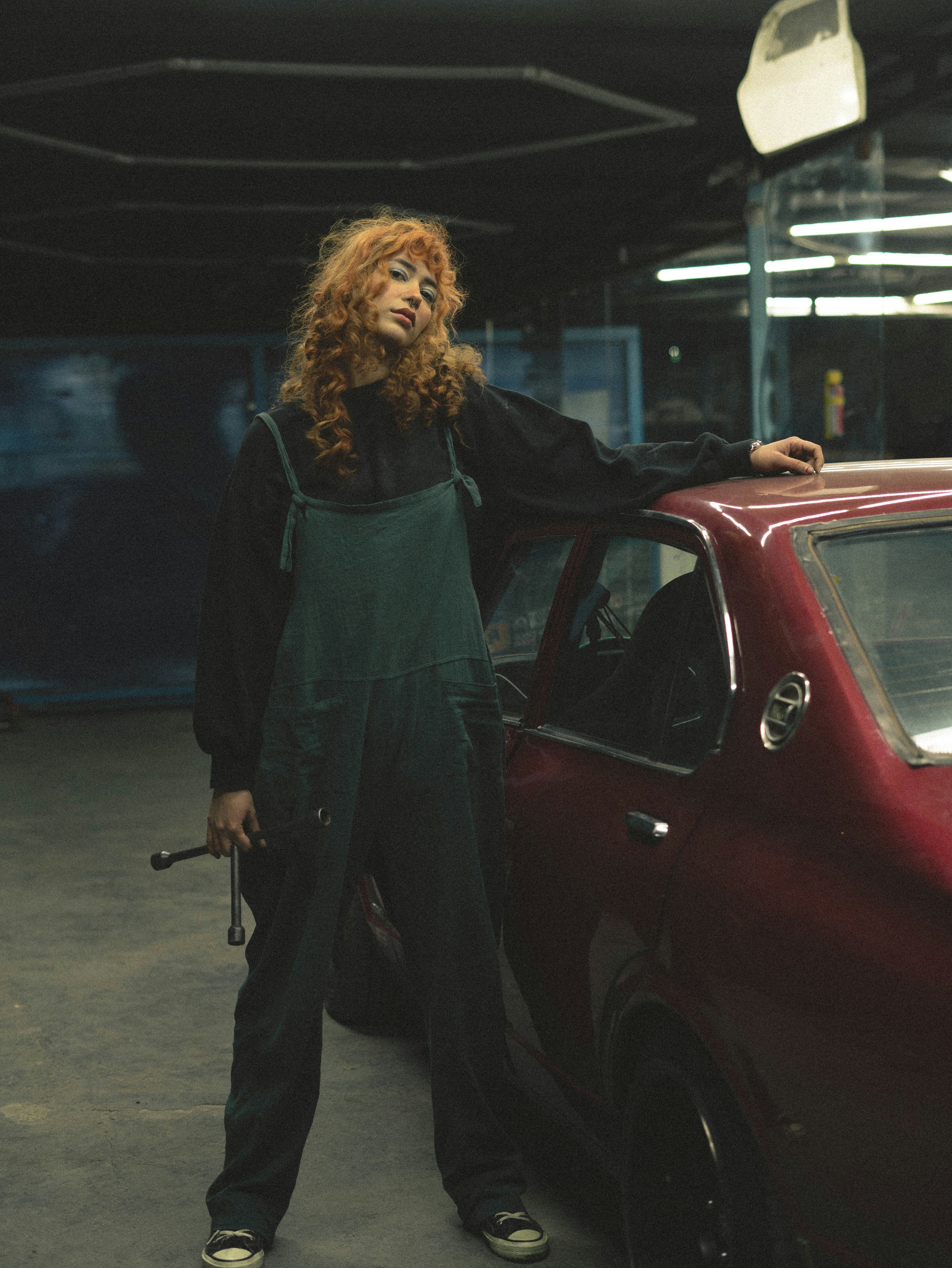 Red-haired woman with wrench leans on vintage car in garage. photo ...