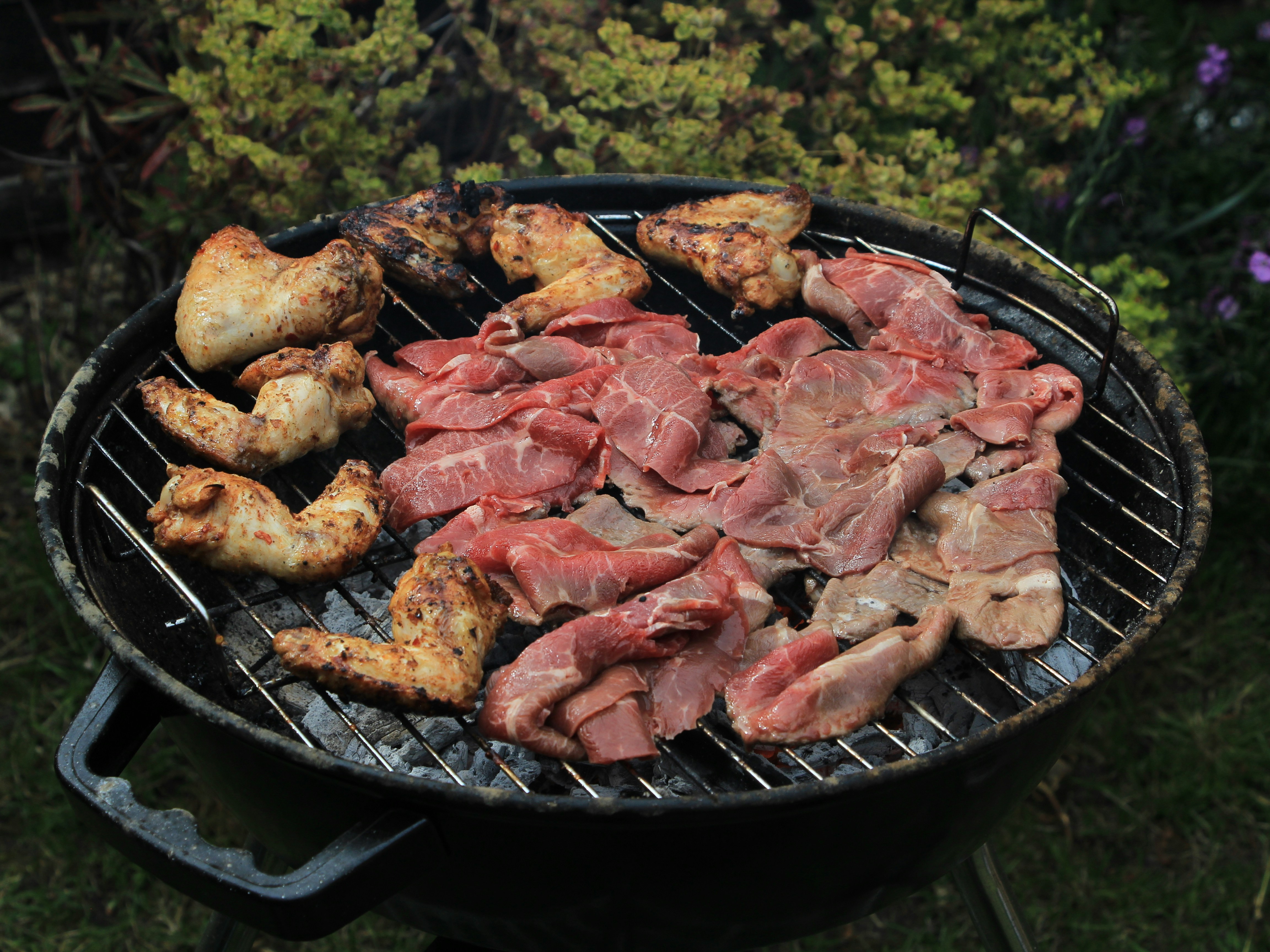 Assorted meats grilling on an outdoor barbecue.
