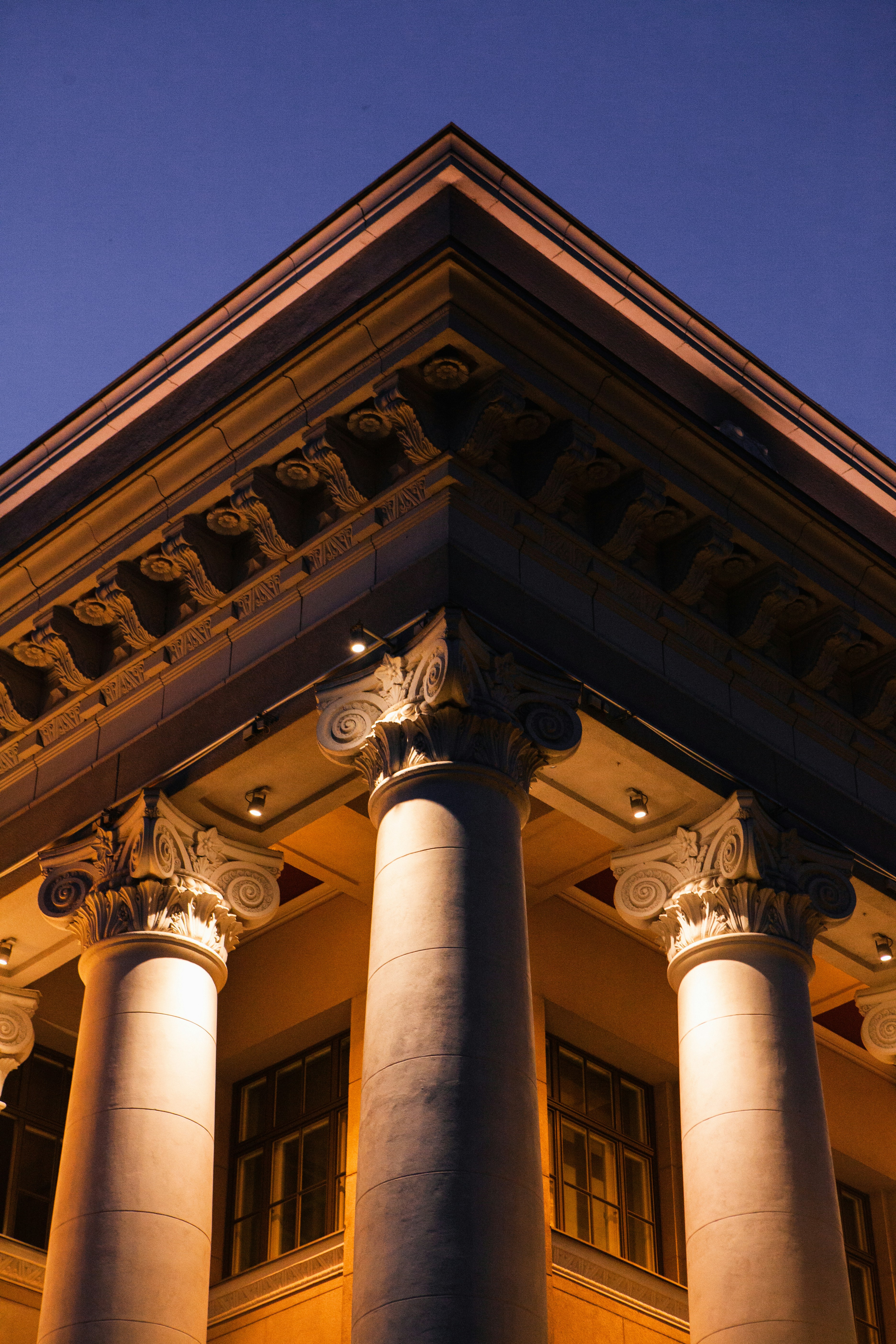 Angle-up view of a neoclassical building facade with prominent columns and ornate capitals, bathed in warm dawn light. Structural details and depth suggest a grand, institutional edifice.
