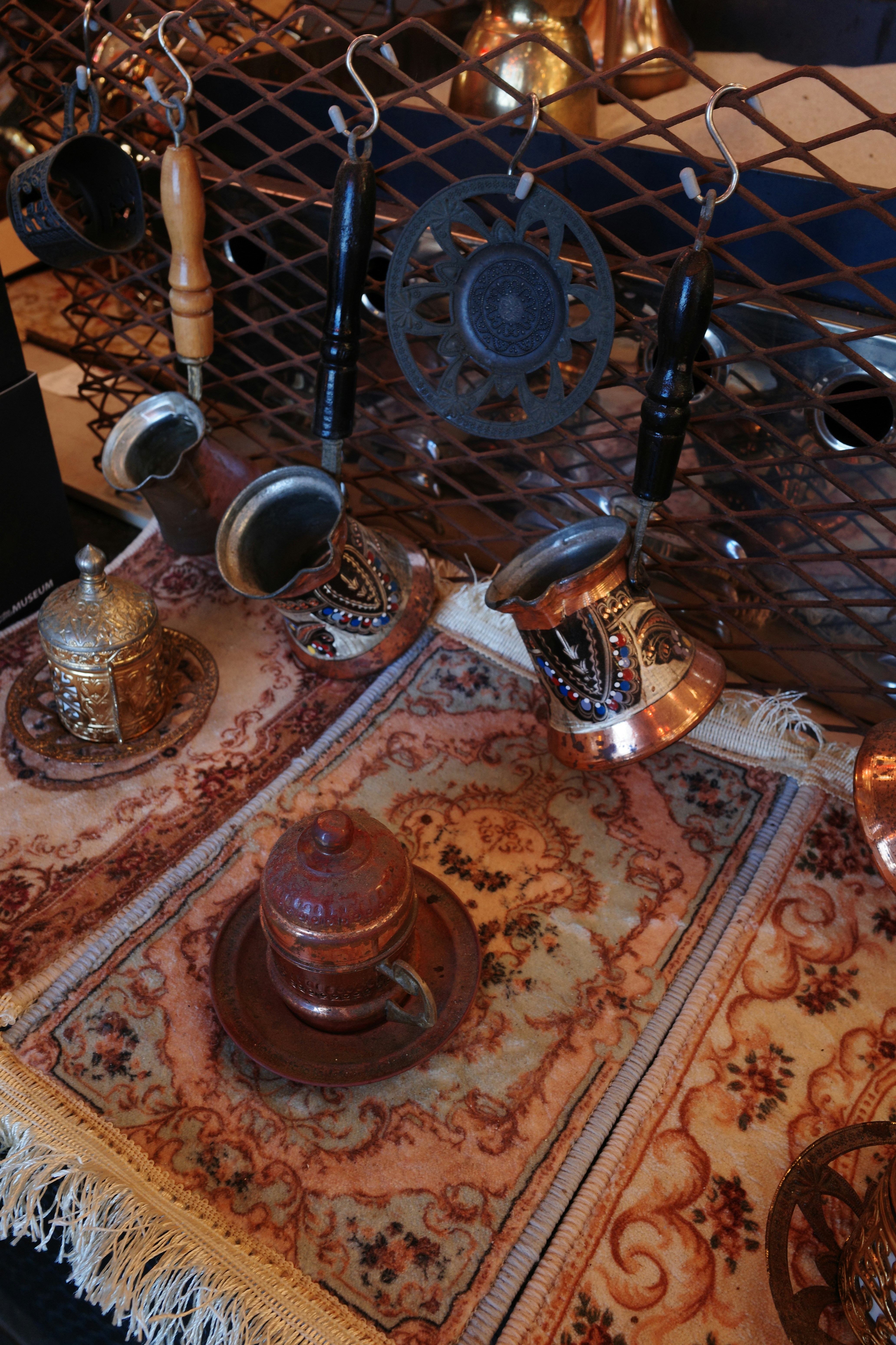 Antique coffee ritual: ornate cezve set on a patterned rug beneath a lattice backdrop