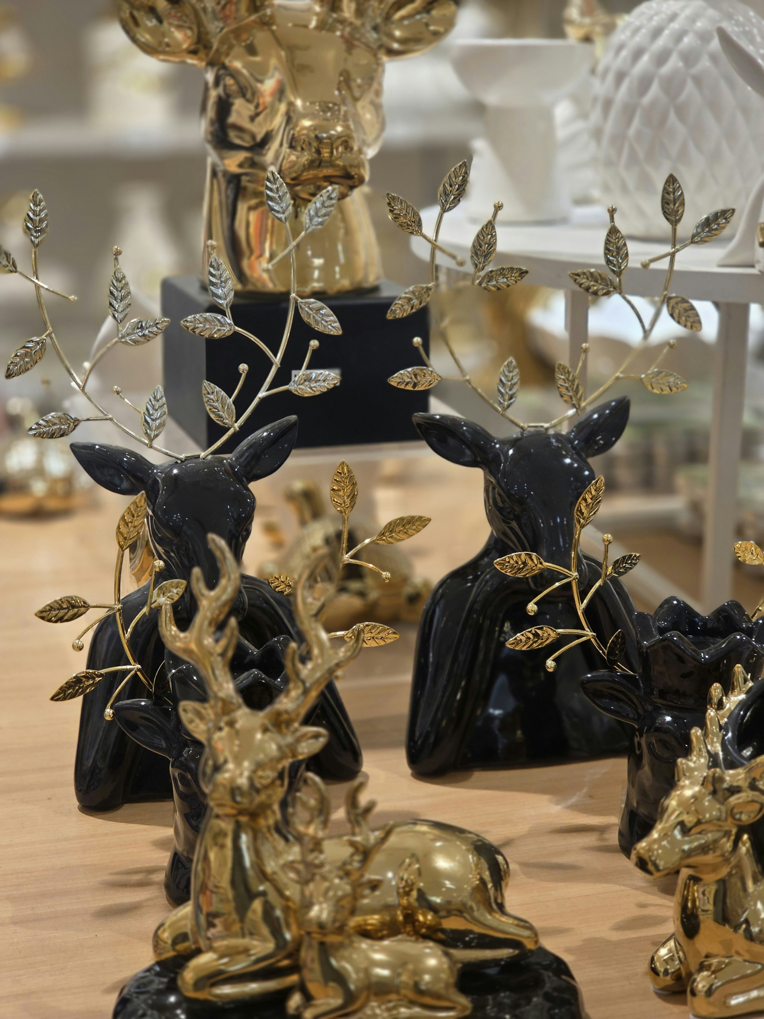 Gold and black deer figurines with delicate leaf accents arranged on a wooden surface in a showroom-like setting.