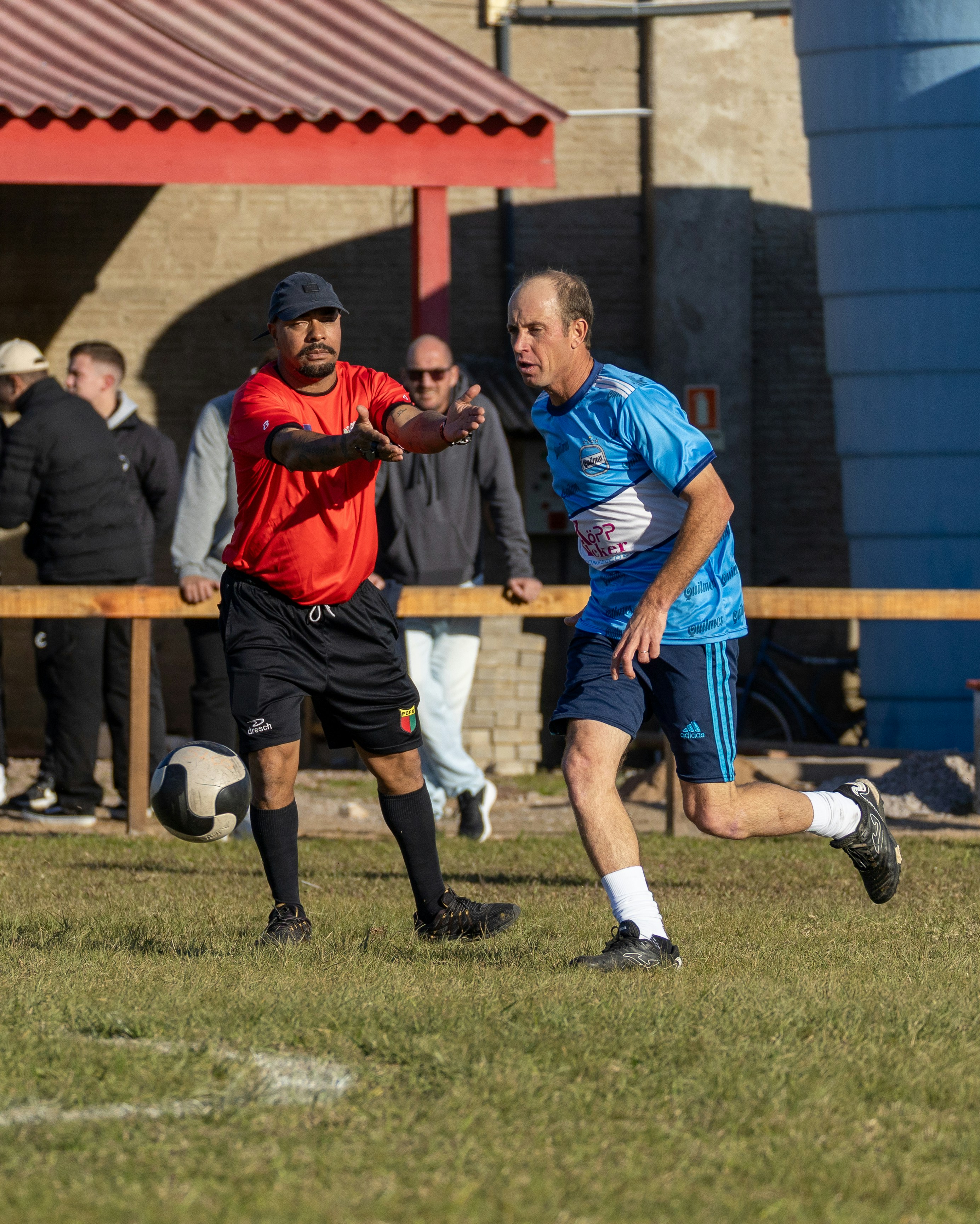 Red-jersey Defender Faces Off Against Blue-jersey Attacker in a Sunny Grass Field