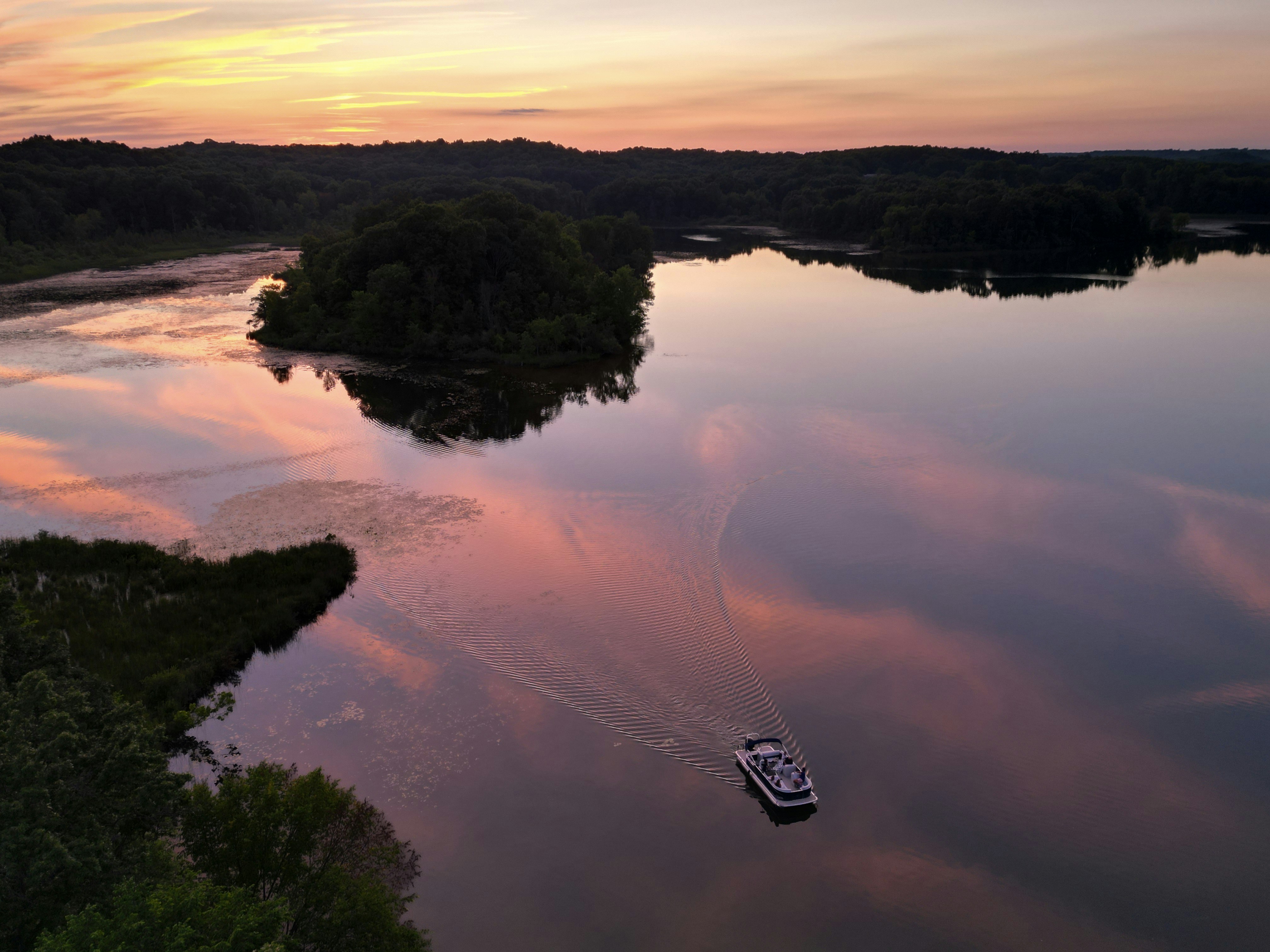 Sunset Overmeandering River: a lone motorboat trails ripples through pastel skies
