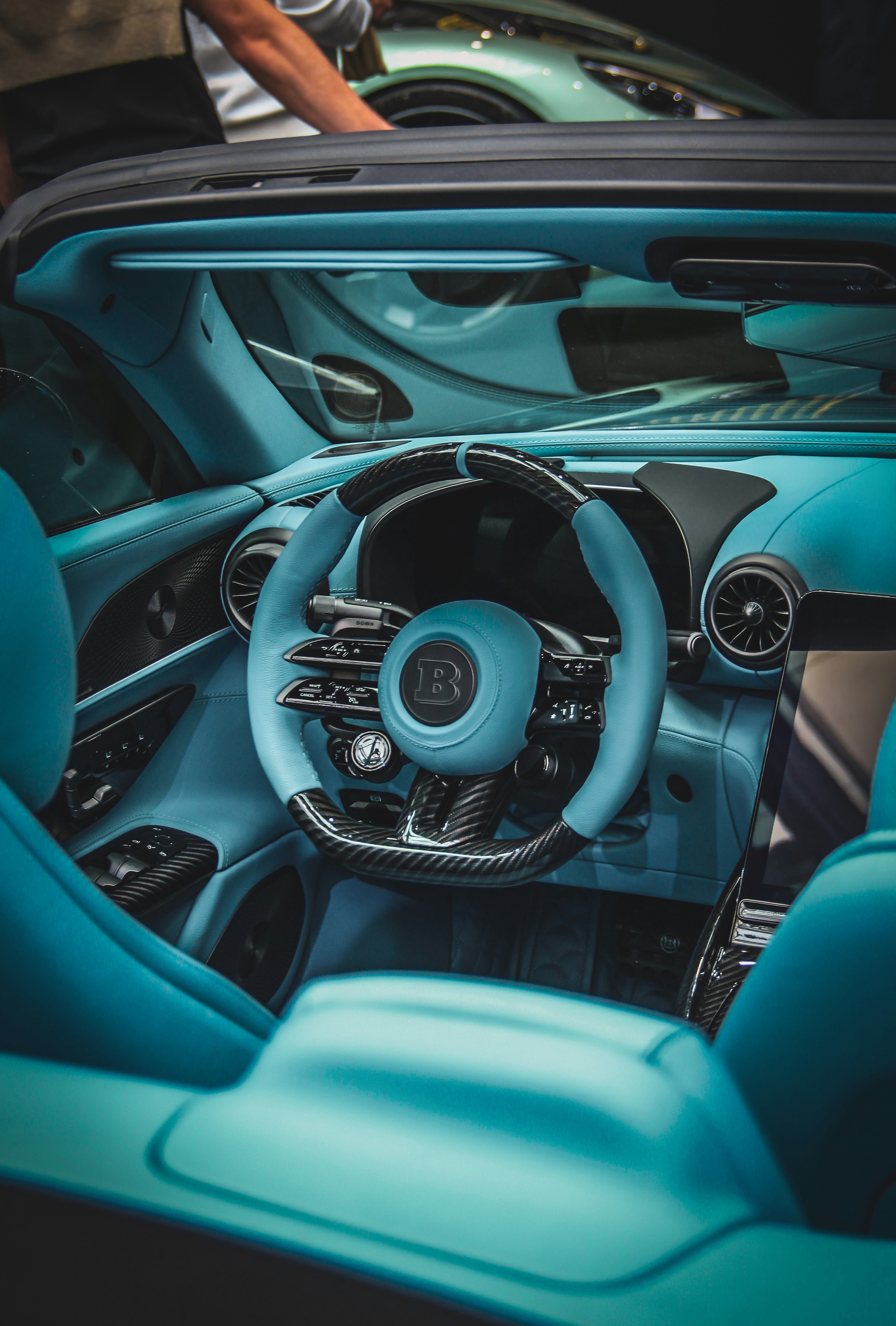 Close-up interior of a turquoise-blue luxury car, highlighting the steering wheel and dashboard with carbon fiber accents.