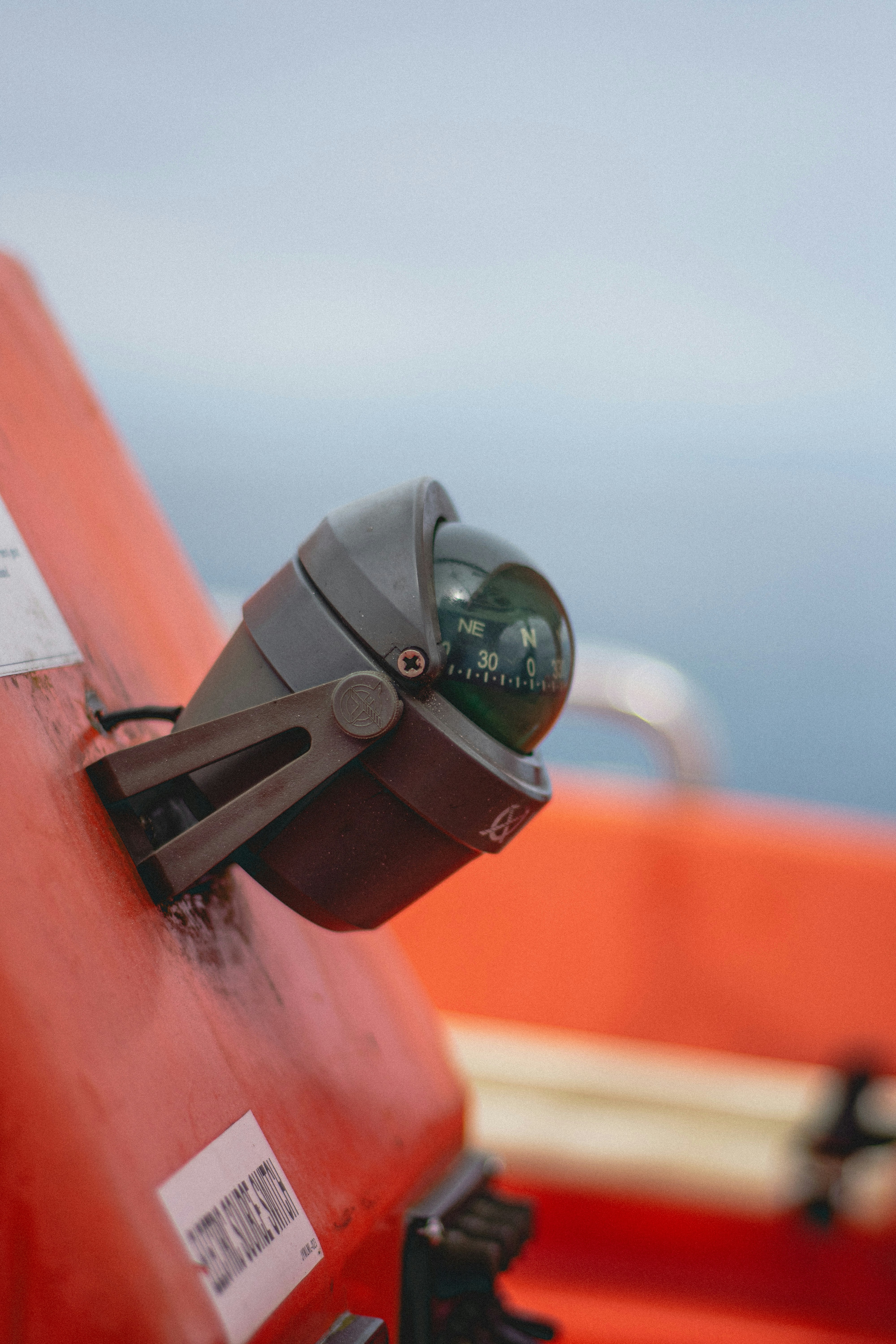 Close-up of an orange lifeboat with a mountable compass, against a blurred blue sea background. The scene emphasizes the gear and its purpose for navigation.