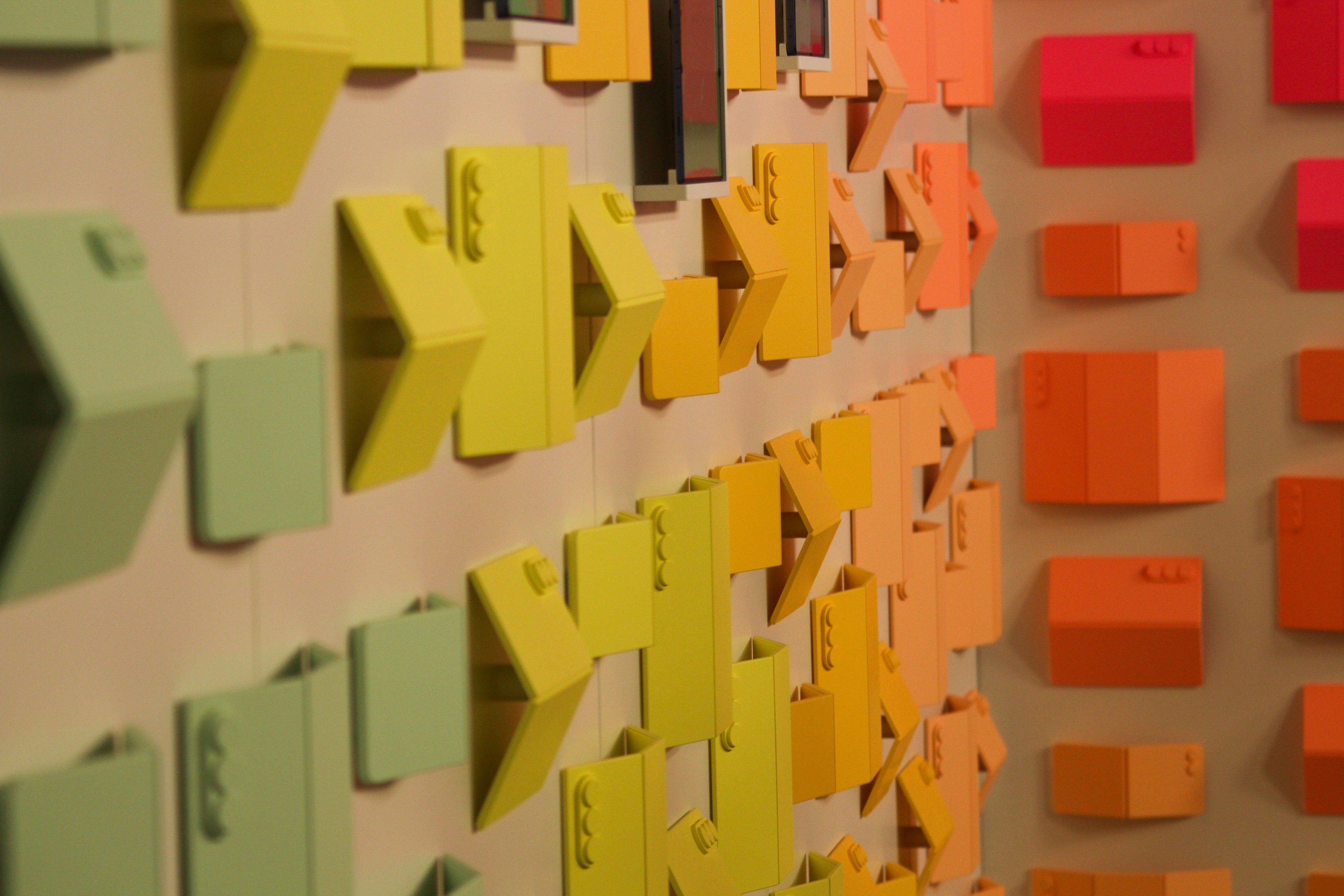 Colorful 3D wall tiles arranged in diagonal bands with pastel greens, yellows, and oranges; shallow depth of field creates a gentle blur across the textured panels.