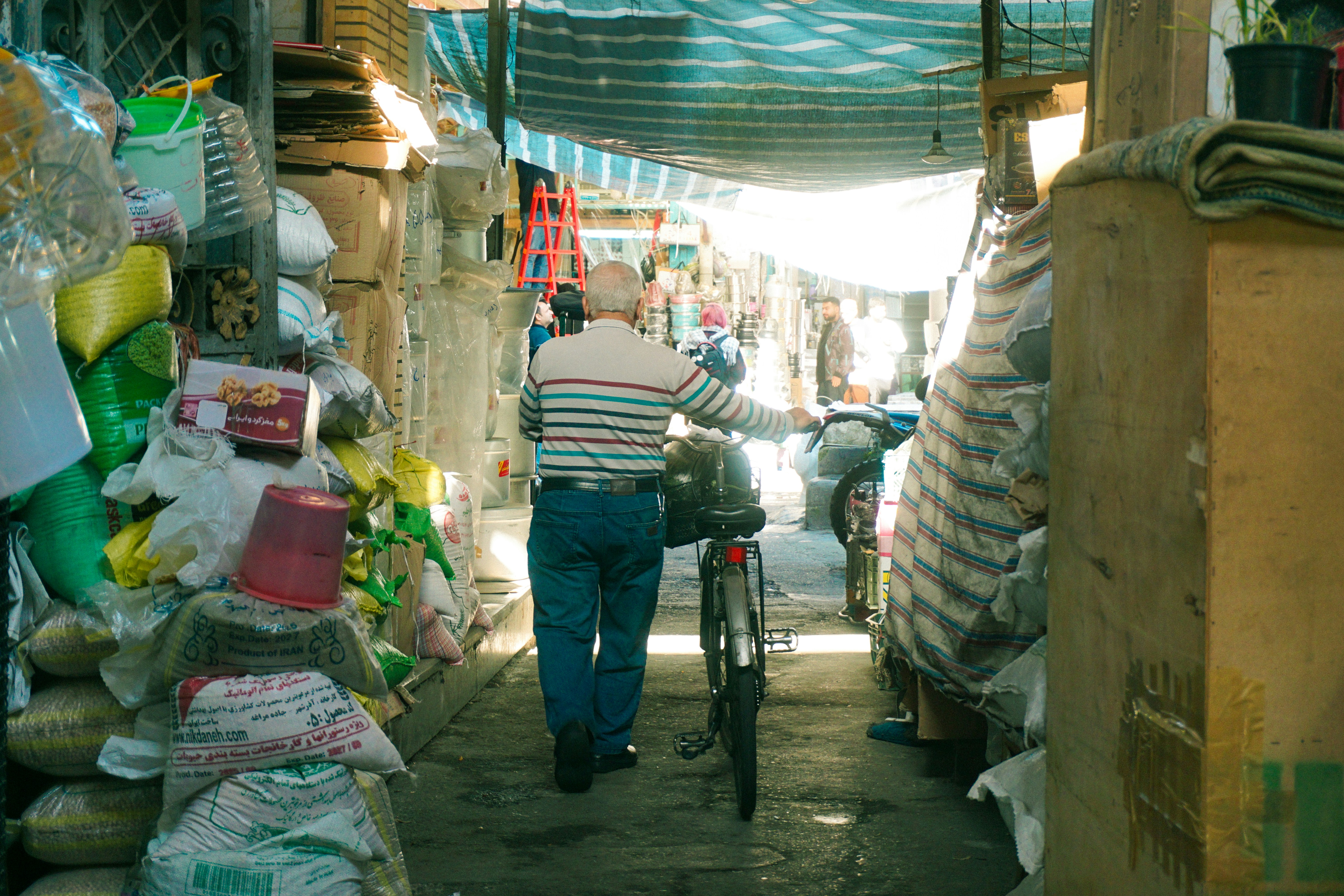 A Quiet Shift: Man with Bicycle in a Narrow Market Alley