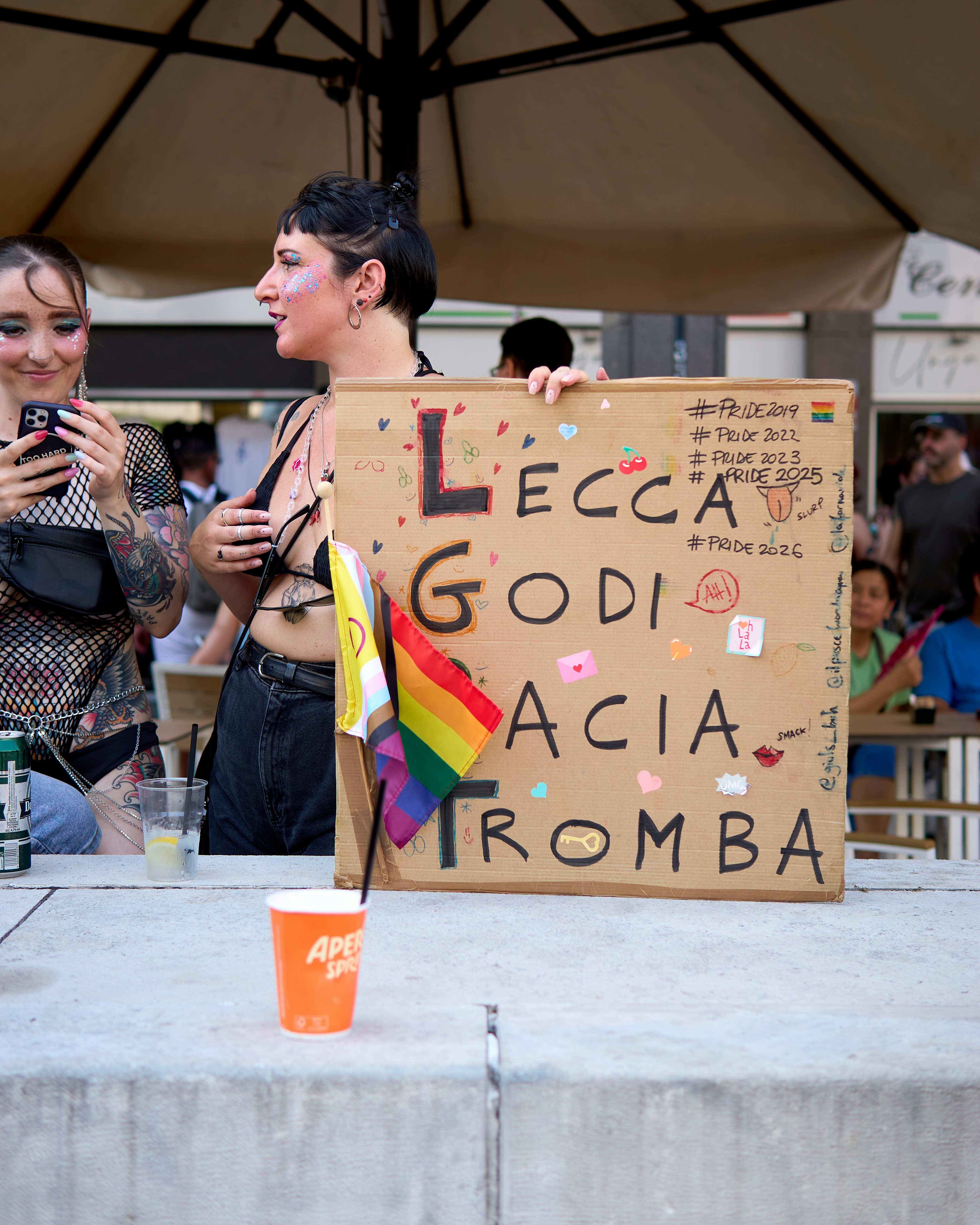 Signage and two revelers at a Pride festival stall