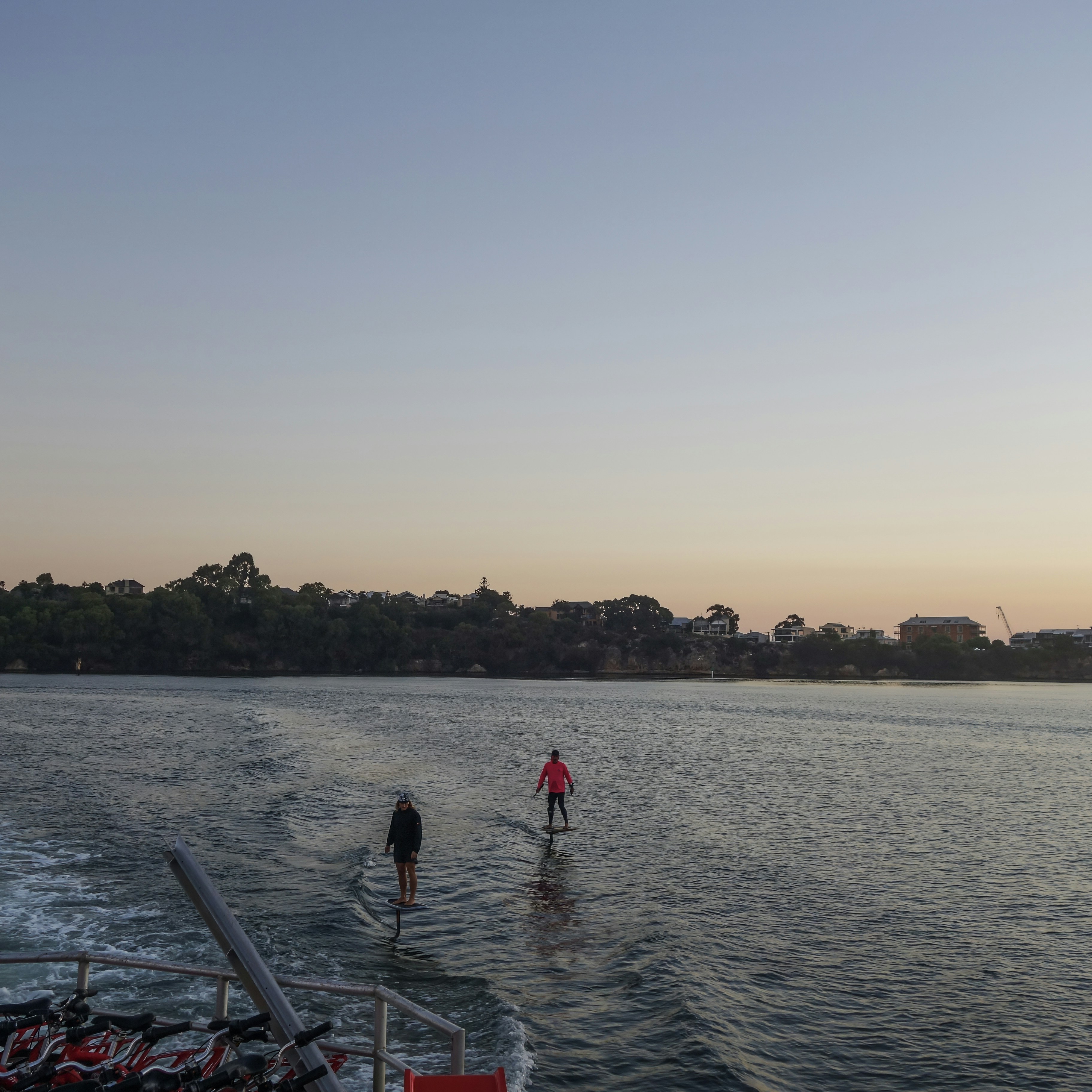 Two stand-up paddle boarders glide across a tranquil harbor at dusk