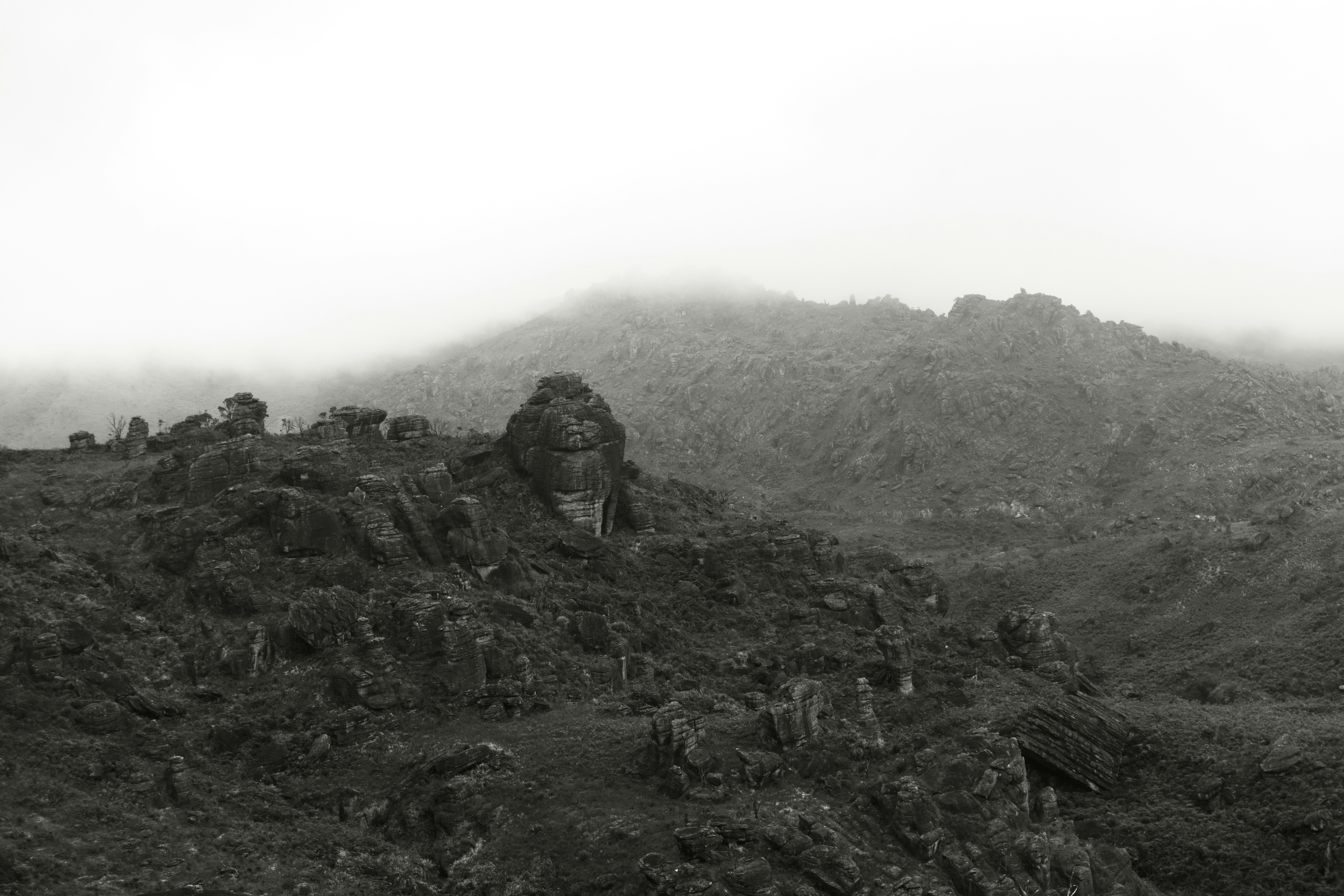 Monochrome landscape of rugged volcanic terrain with a lone, weathered statue emerging from the rocks, shrouded by low-lying mist.