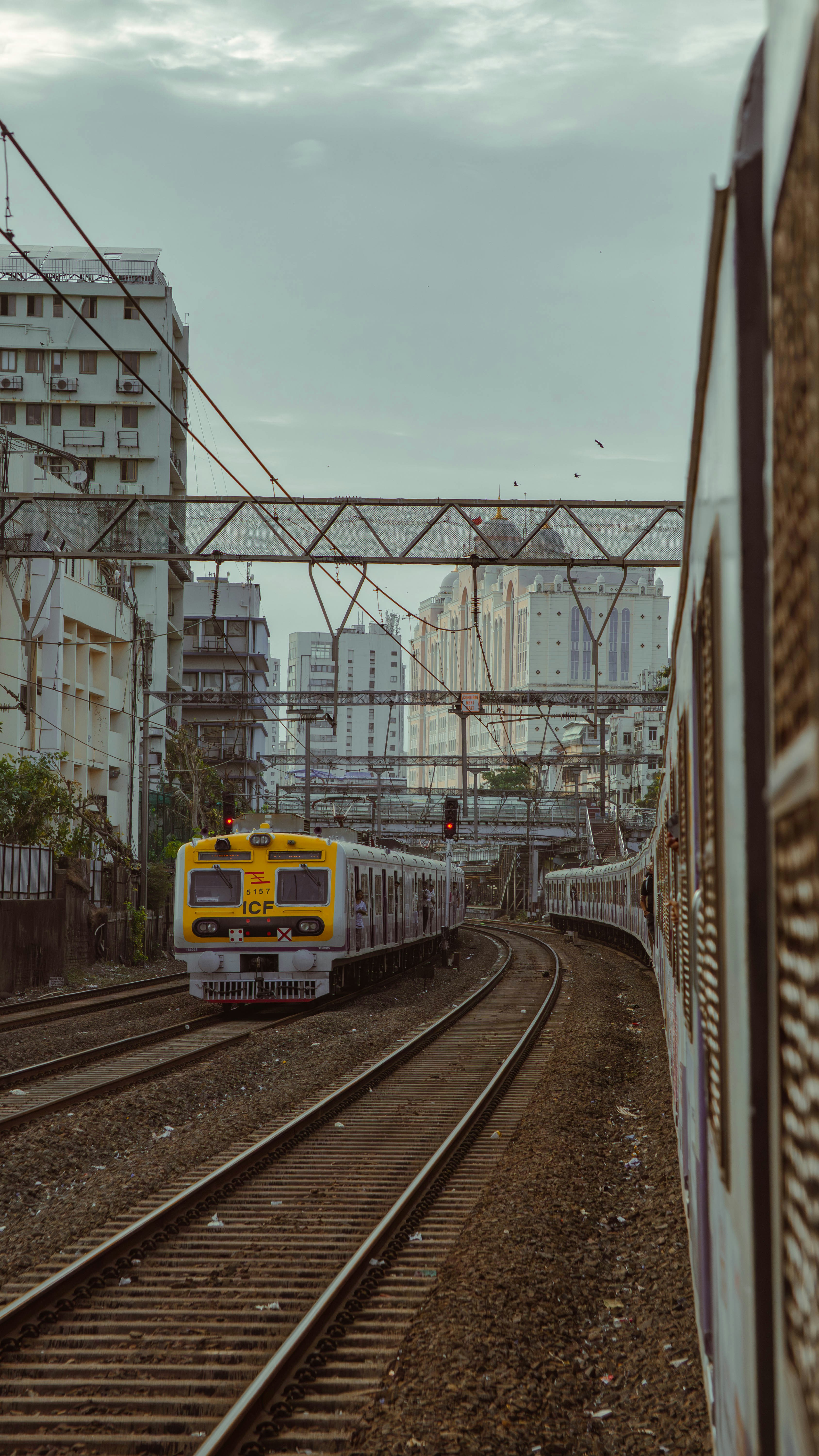 Urban railway scene with a yellow locomotive leading a passenger train along curved tracks between tall buildings; a sense of motion and metropolitan scale. (Photo, not a logo or illustration.)