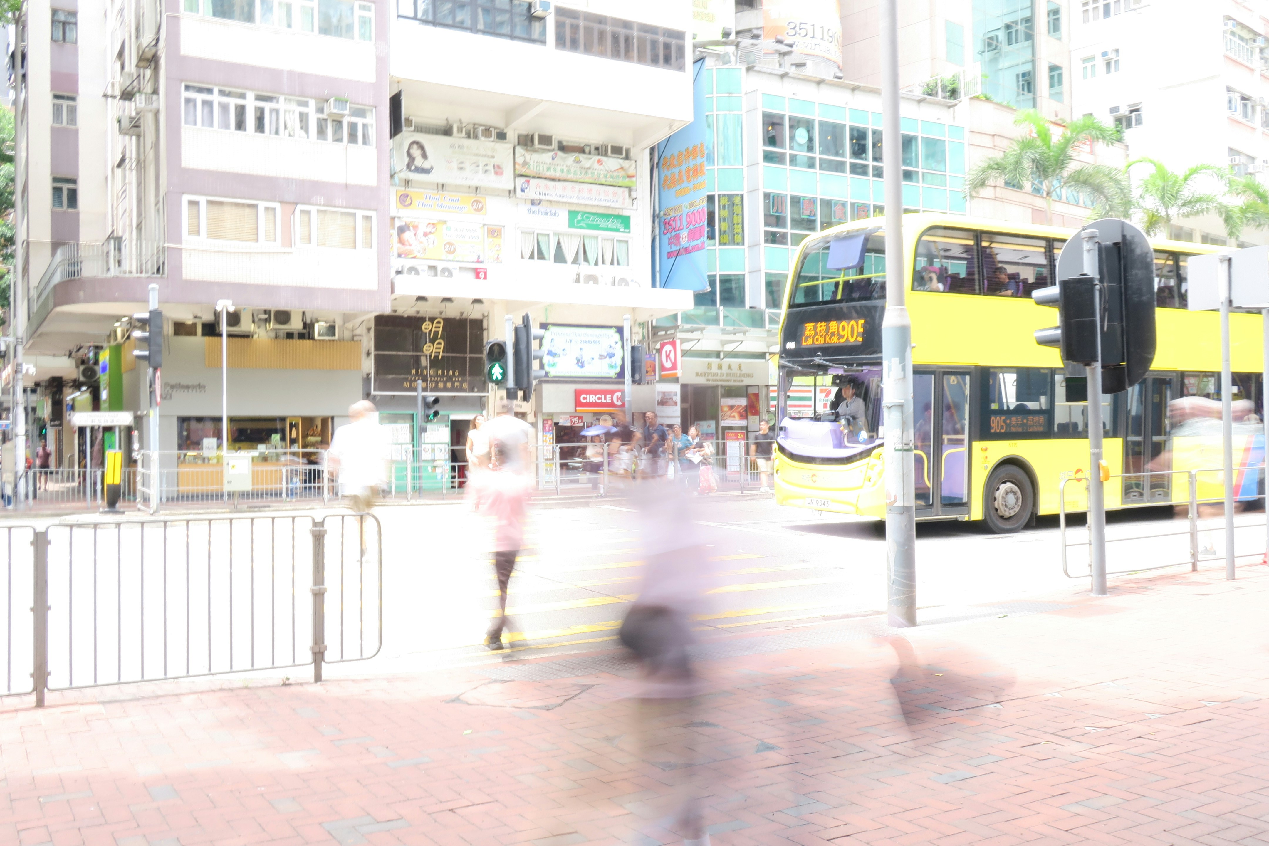 Urban street scene with a bright yellow bus and blurred pedestrians at crosswalk; motion blur conveys rapid movement in a city environment.