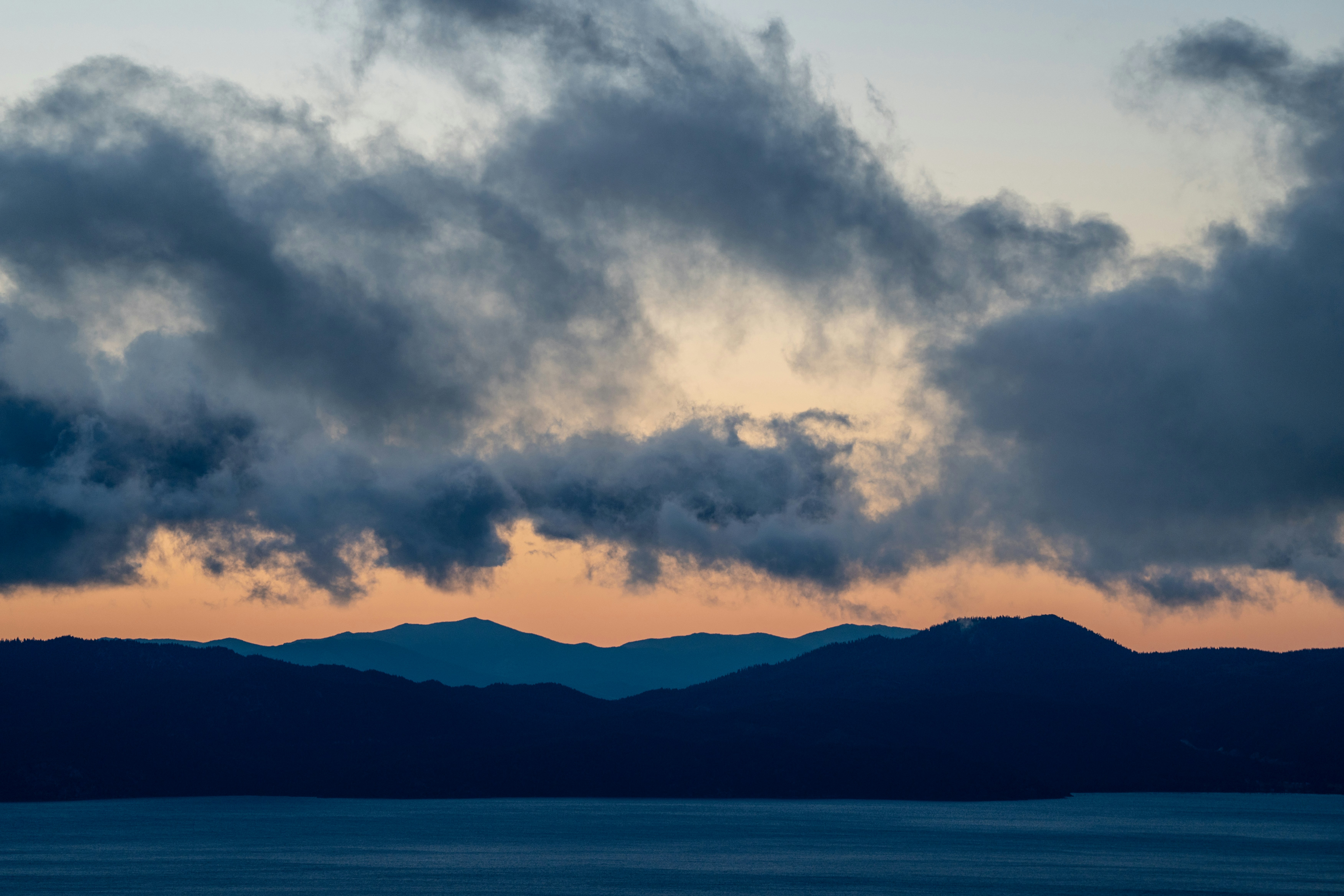 Soft-contrast sunset over distant ridge with layered mountains and a calm body of water; a tranquil landscape emphasizing horizon glow. (Photo shows a natural scenery, not a logo or illustration.)