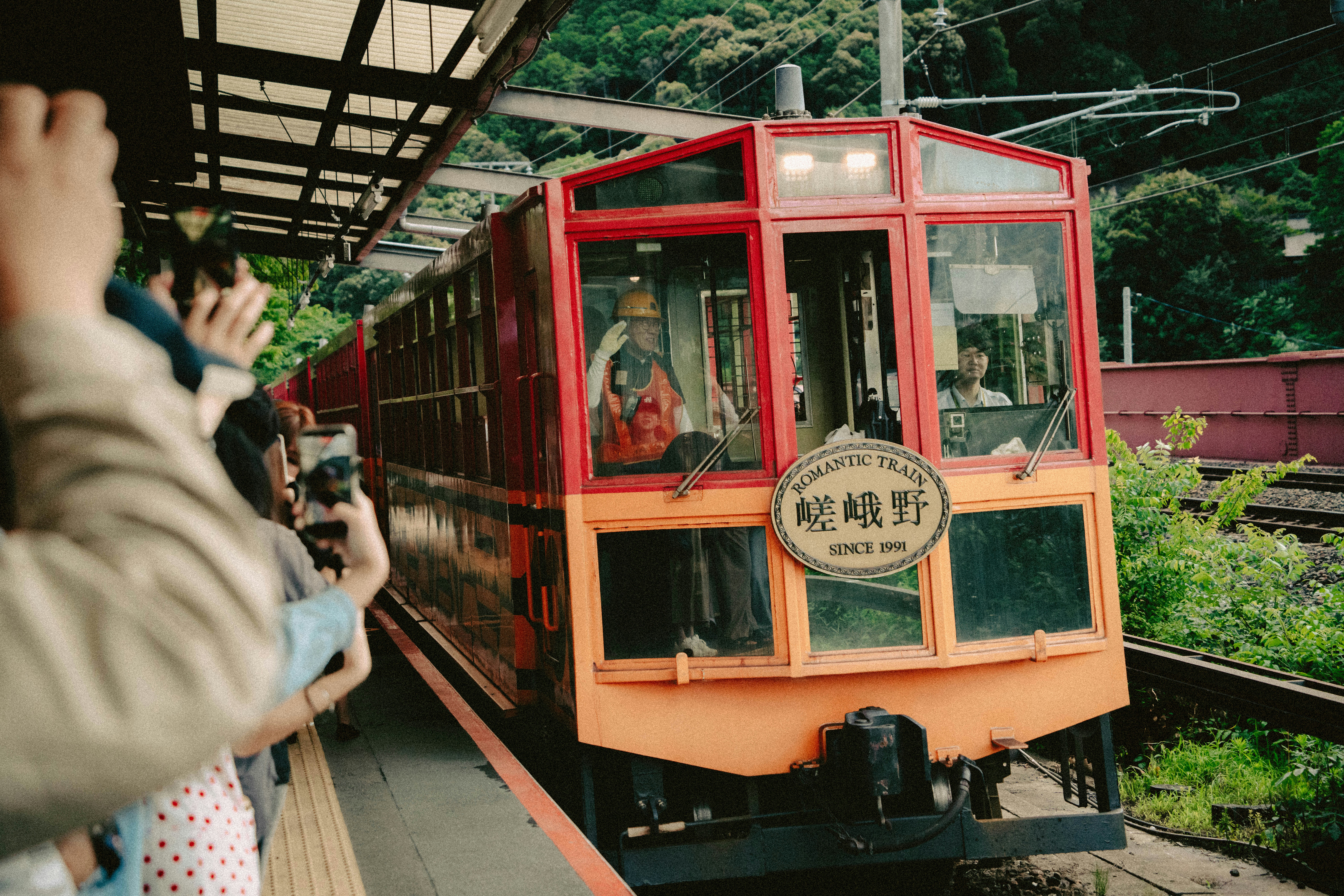 Old red funicular pulls into the platform while a crowd captures the moment