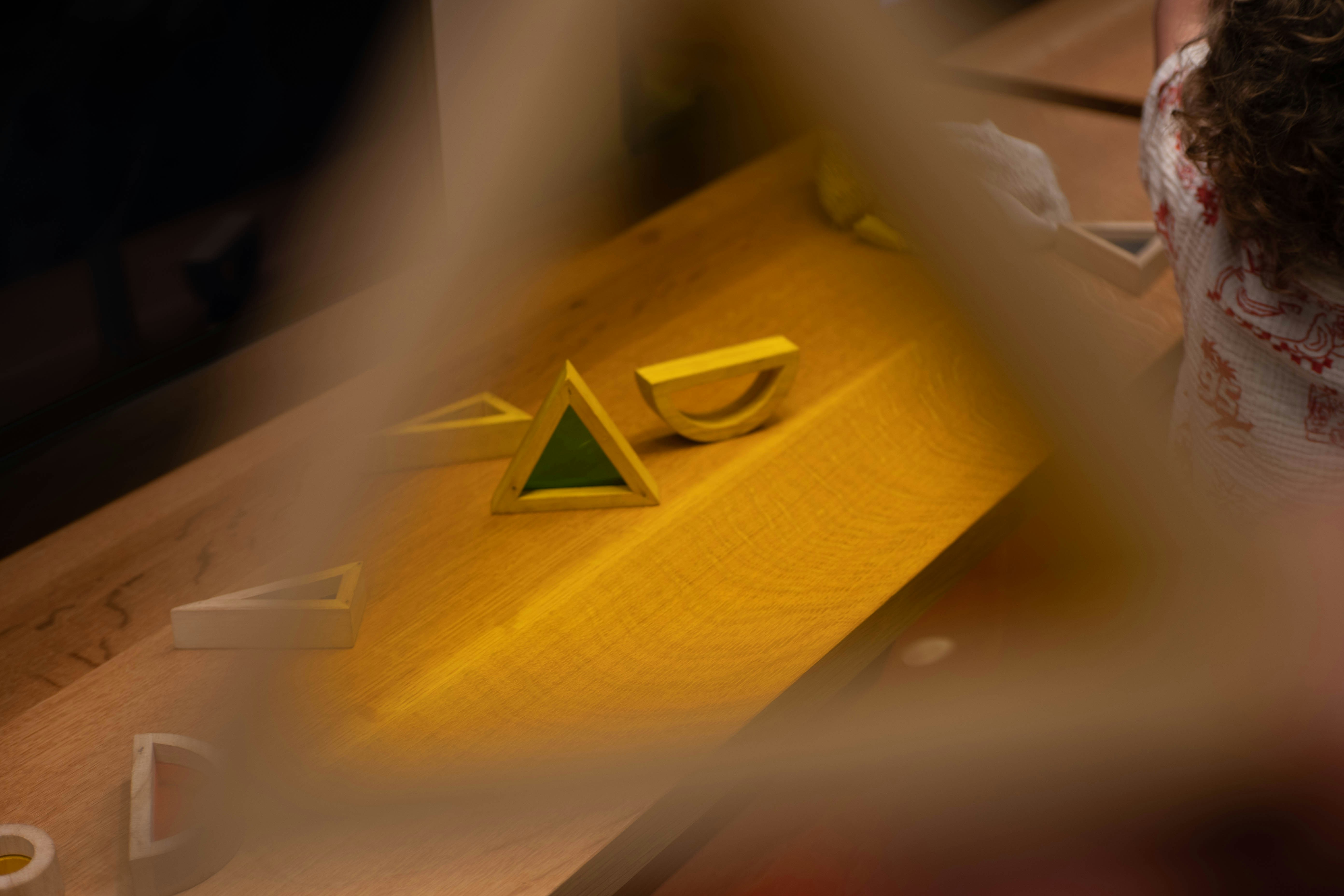 Geometric green triangle on a warm wooden table viewed through a soft aperture