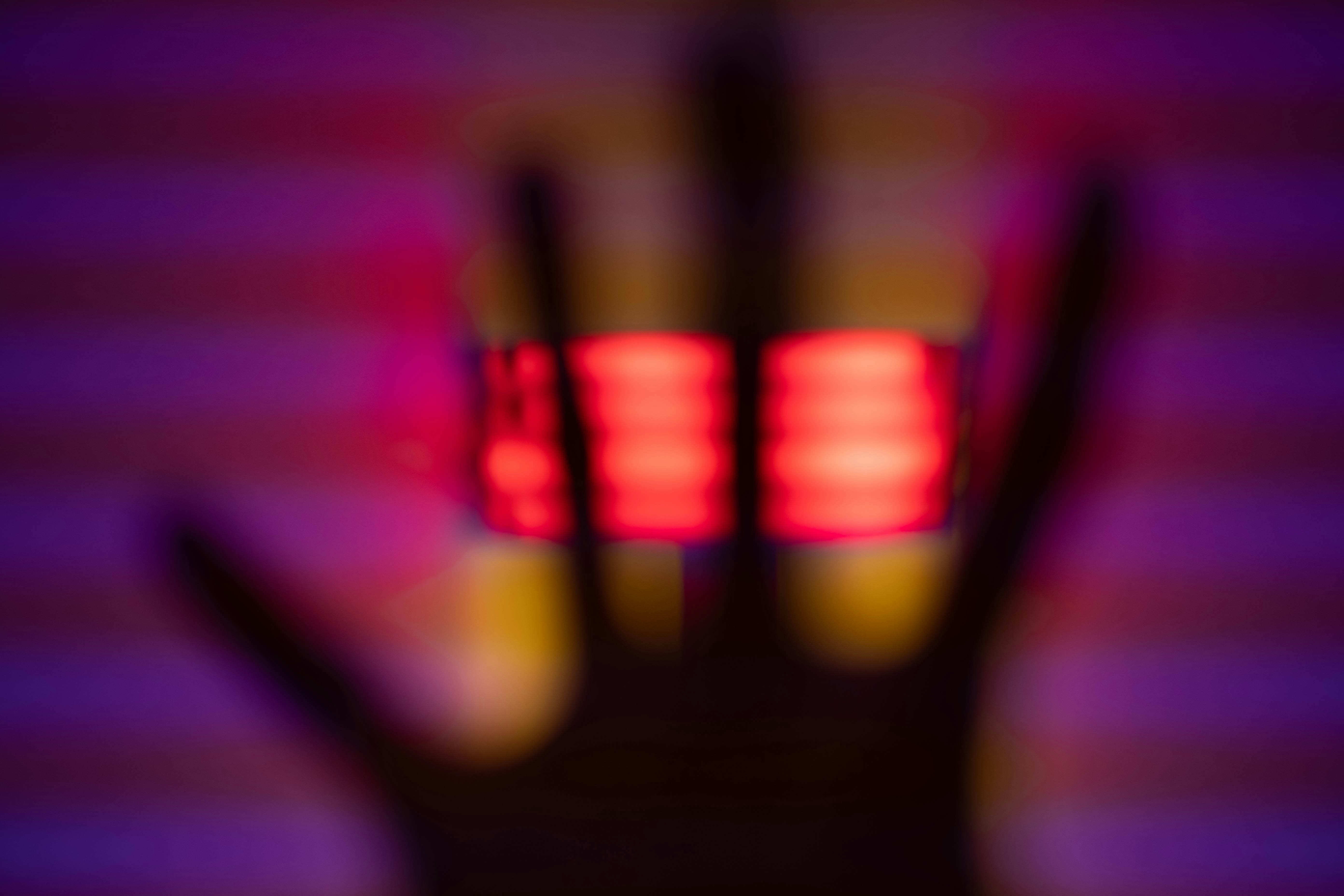 Blurred neon-lit glove pressed against a striped background, creating an abstract silhouette and color glow. This is a photographic study emphasizing color and shape; a sensory, non-literal composition.