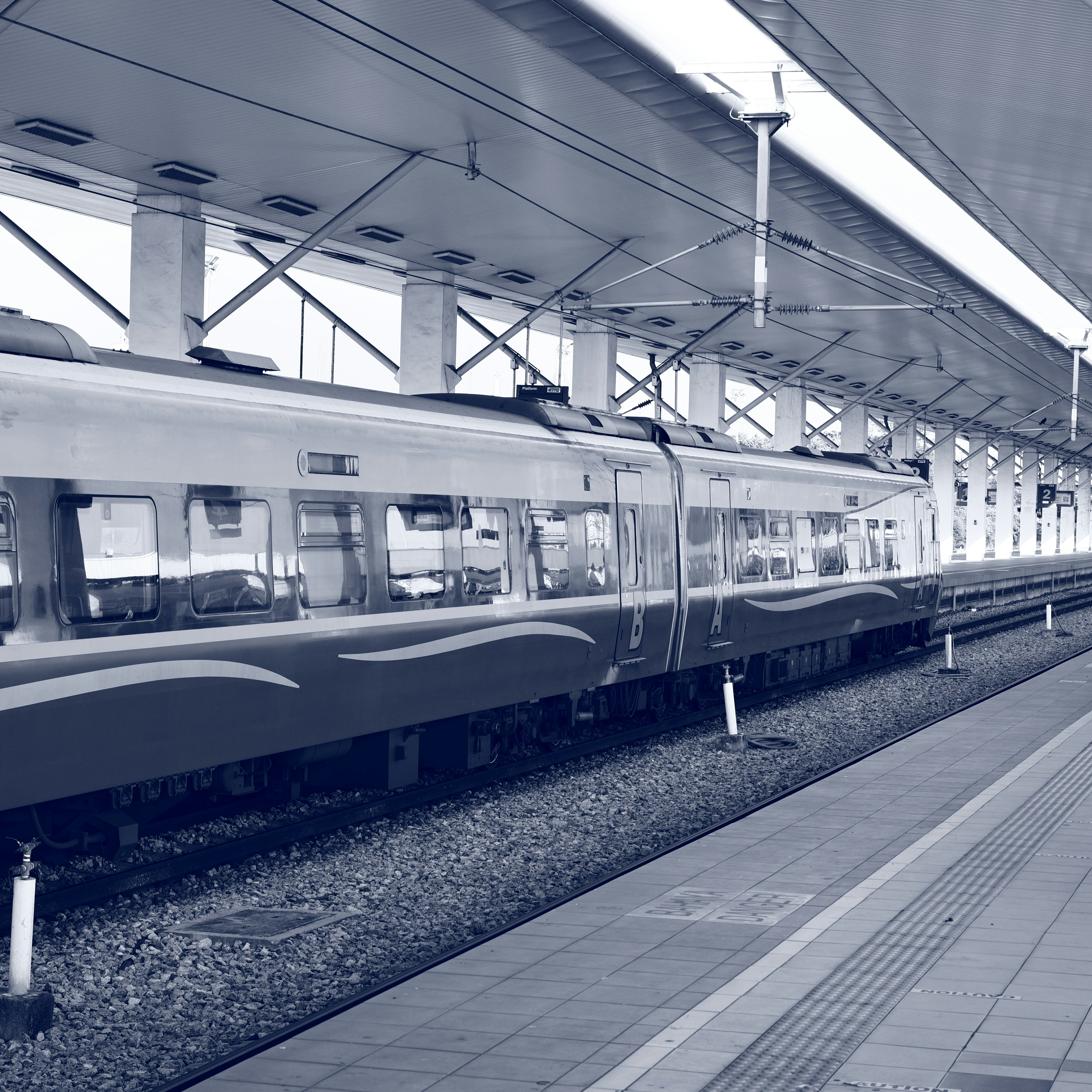 Long, modern train at a station platform with clean lines and a blue-toned monochrome palette.