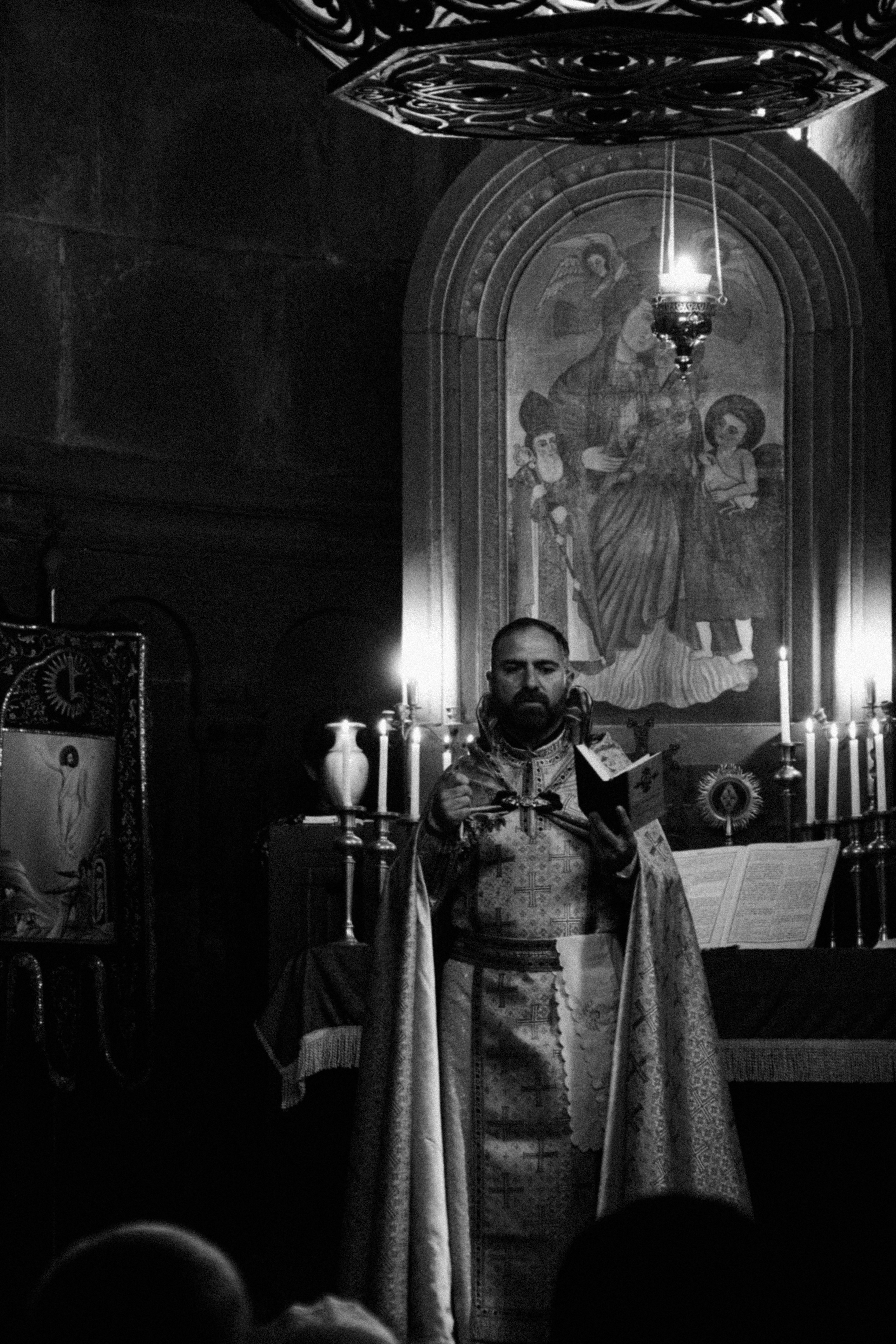 A priest in solemn light reads from a liturgical book beneath a sacred icon