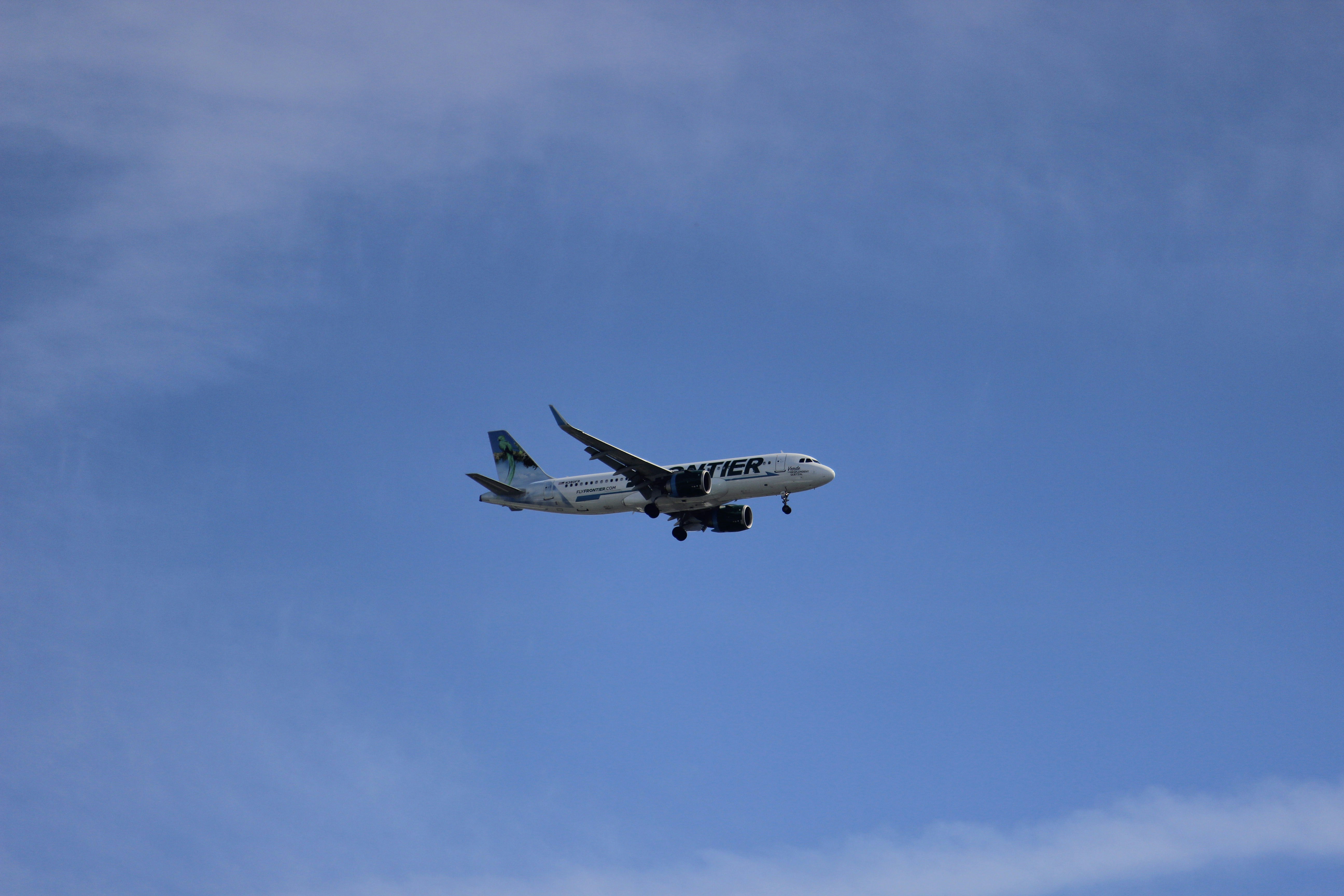 Airplane descends through a blue sky with light clouds, captured mid-flight with landing gear visible; a crisp, uncluttered sky emphasizes the aircraft against the backdrop. Photograph likely from a distant vantage point.