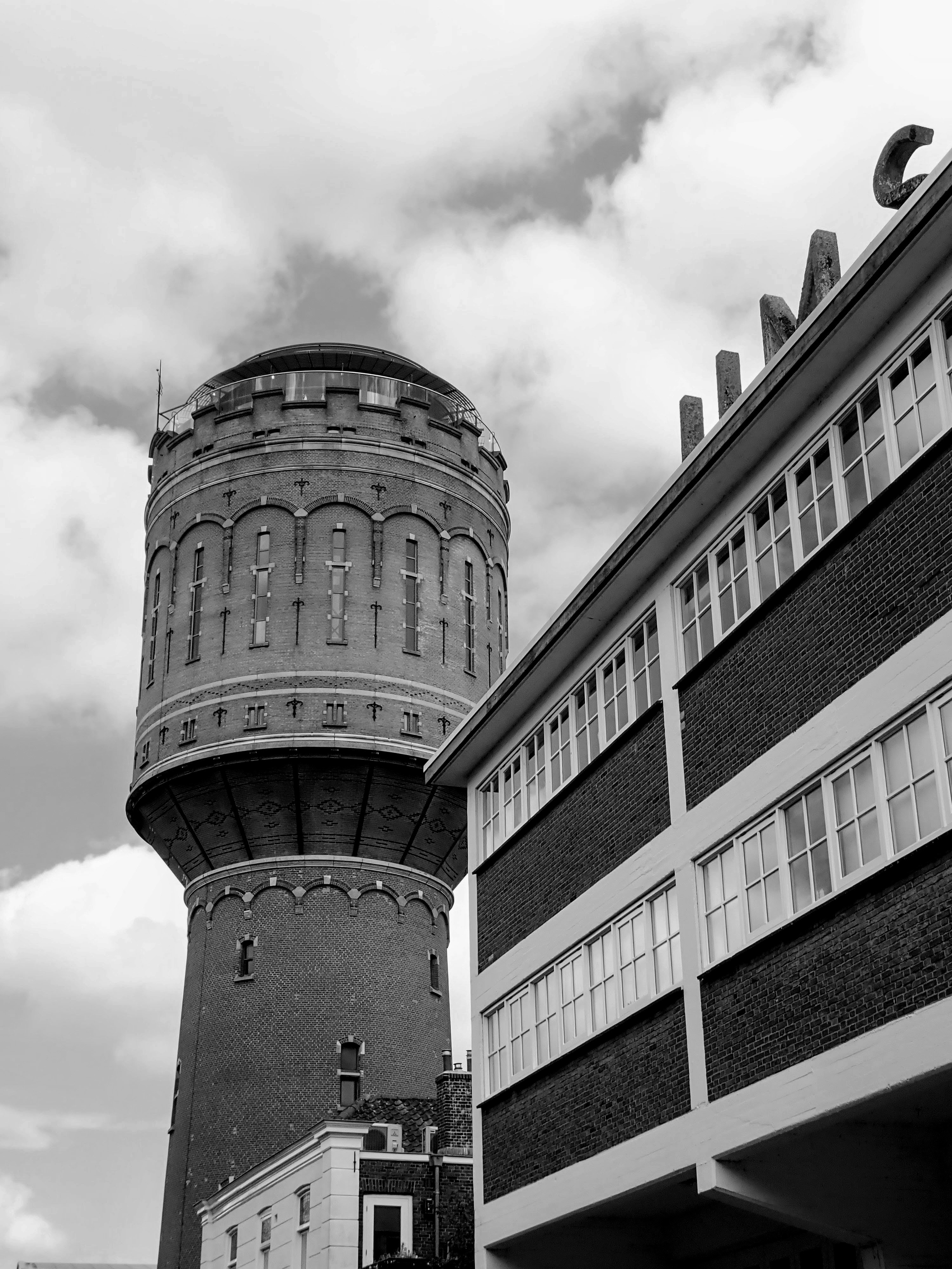 Monochrome scene depicting a historic water tower adjacent to a modern brick-and-glass building, highlighting contrast in architectural styles.