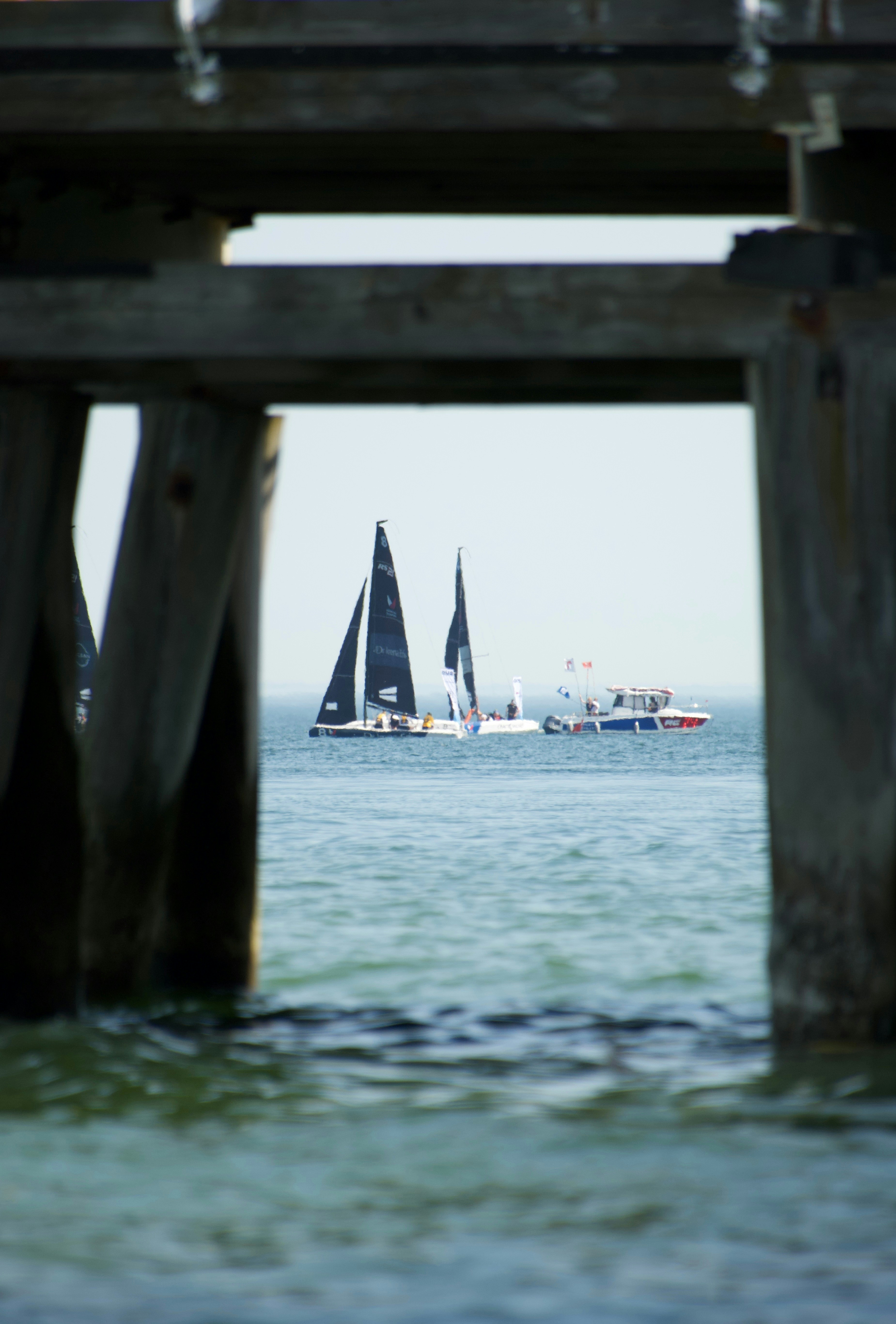 Between the Pilings: Sailboats framed by the pier’s weathered silhouette
