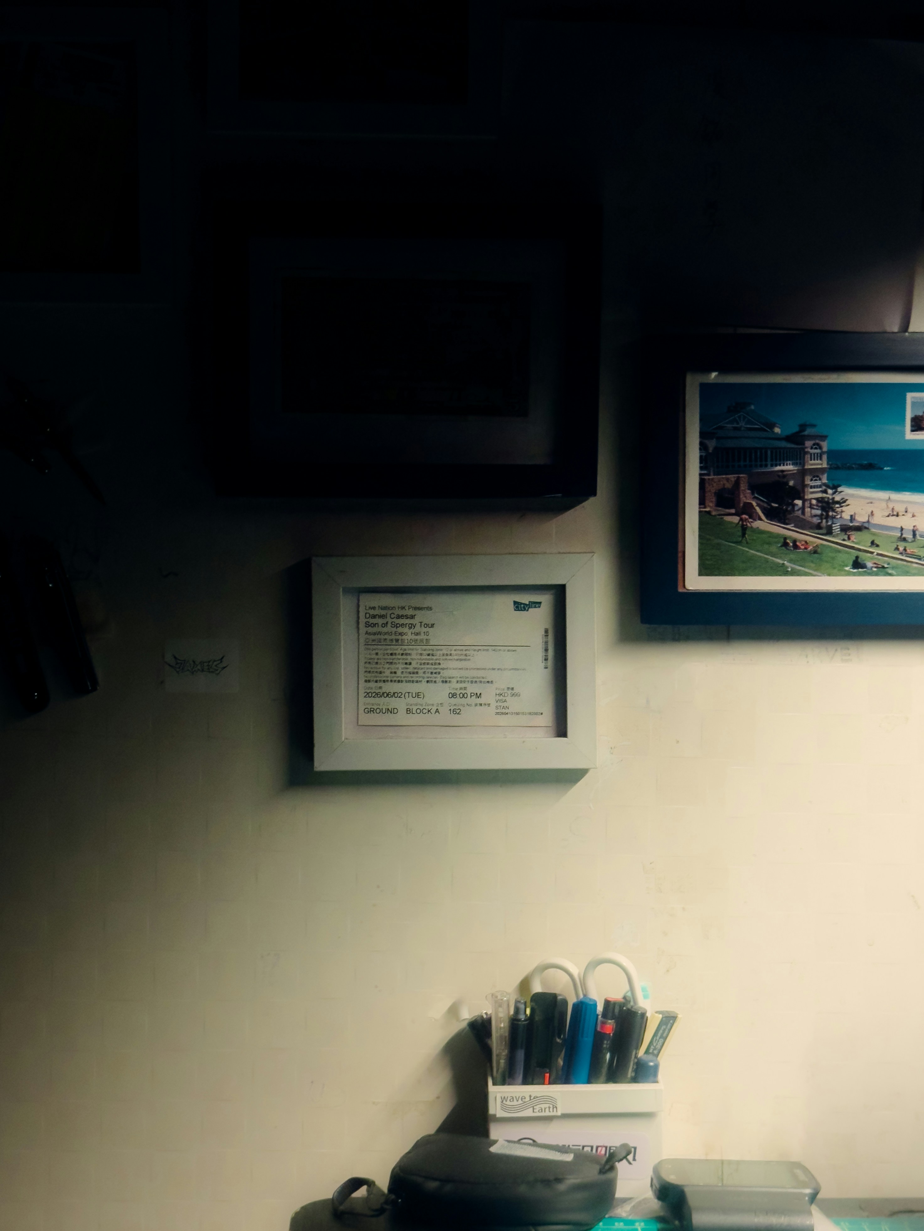 Dimly lit interior featuring a wall with framed pictures and a small collection of pens in a holder atop a desk, conveying a quiet, personal workspace.