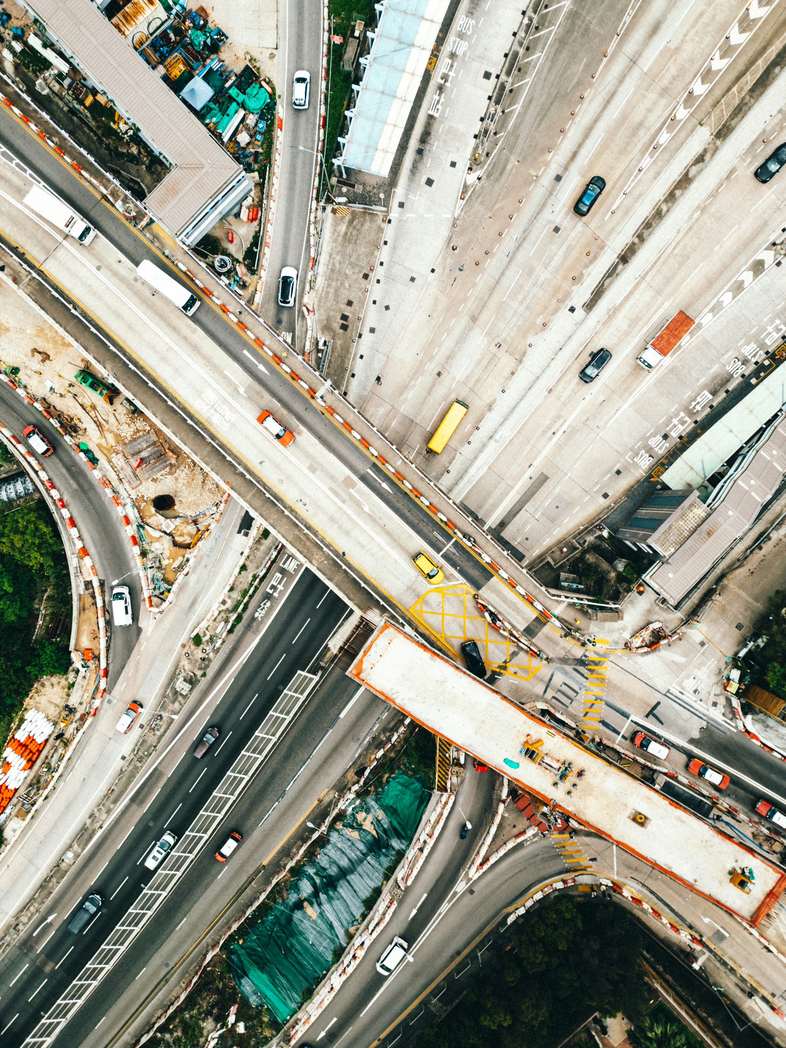 Aerial view of a complex highway interchange with intertwined ramps and overpasses, showing dense urban traffic and construction elements in a bird’s-eye perspective.