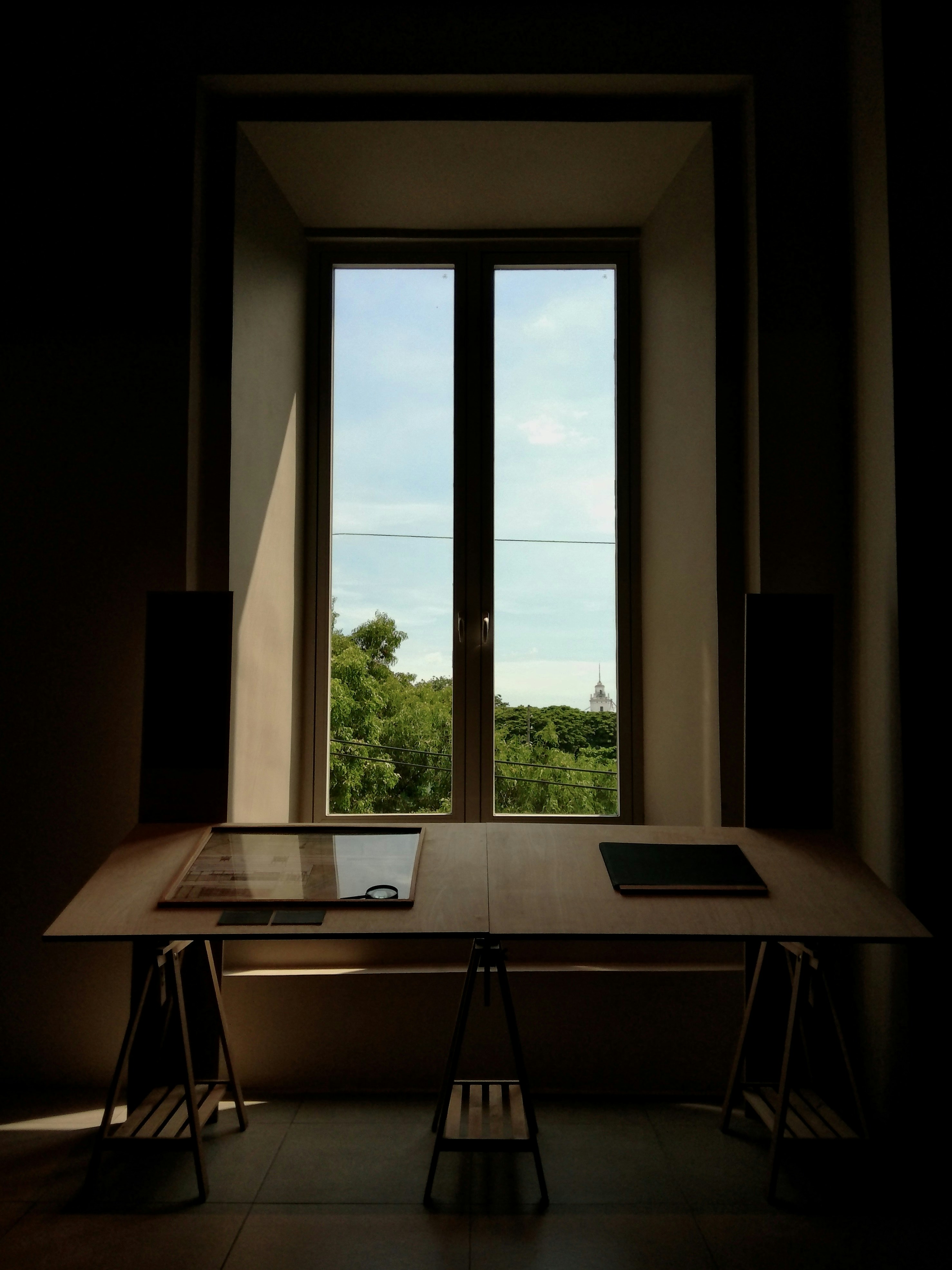 A dark room with a bright window overlooking green trees.