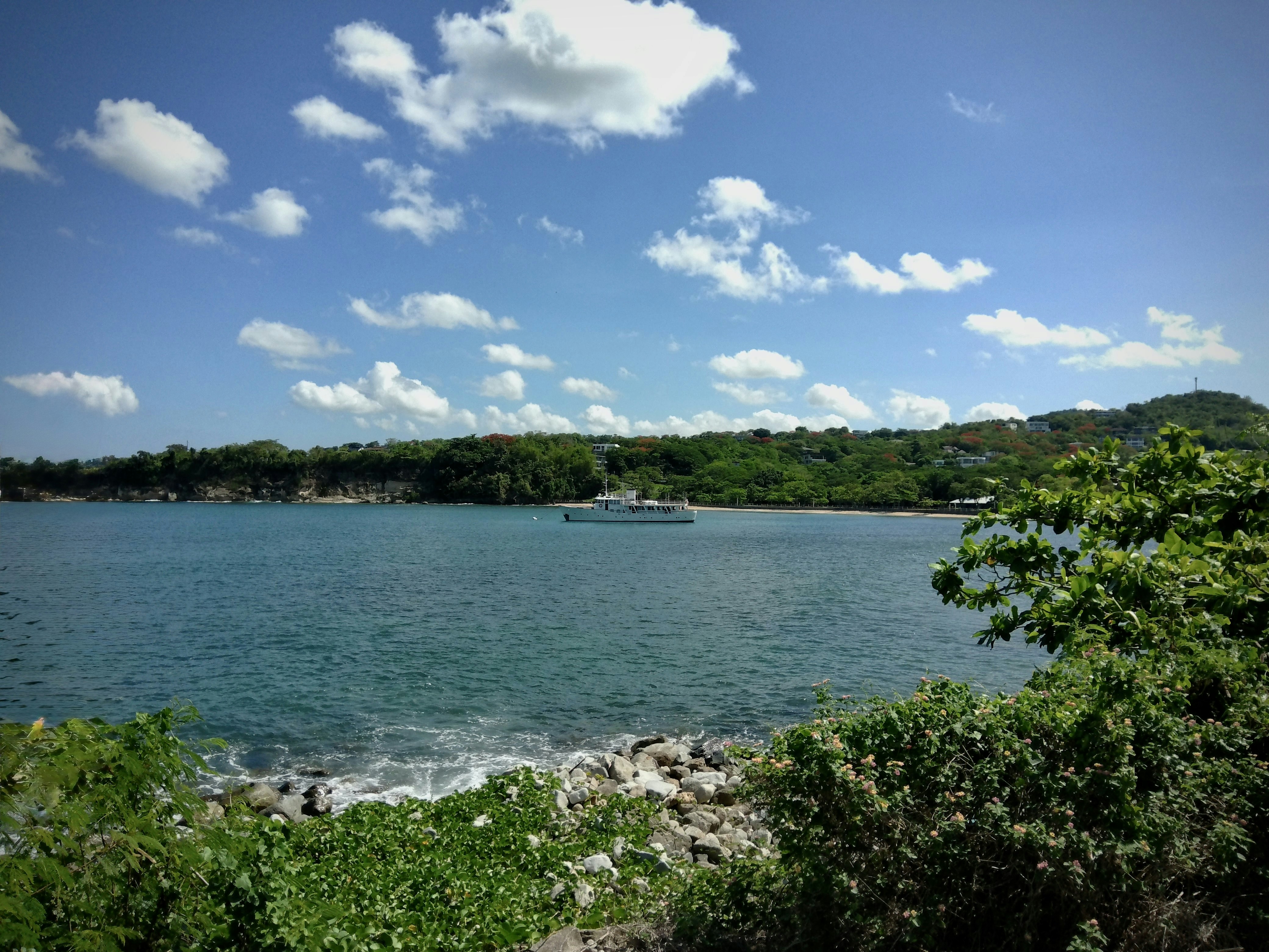 Scenic bay with a boat, green hills, and blue sky.