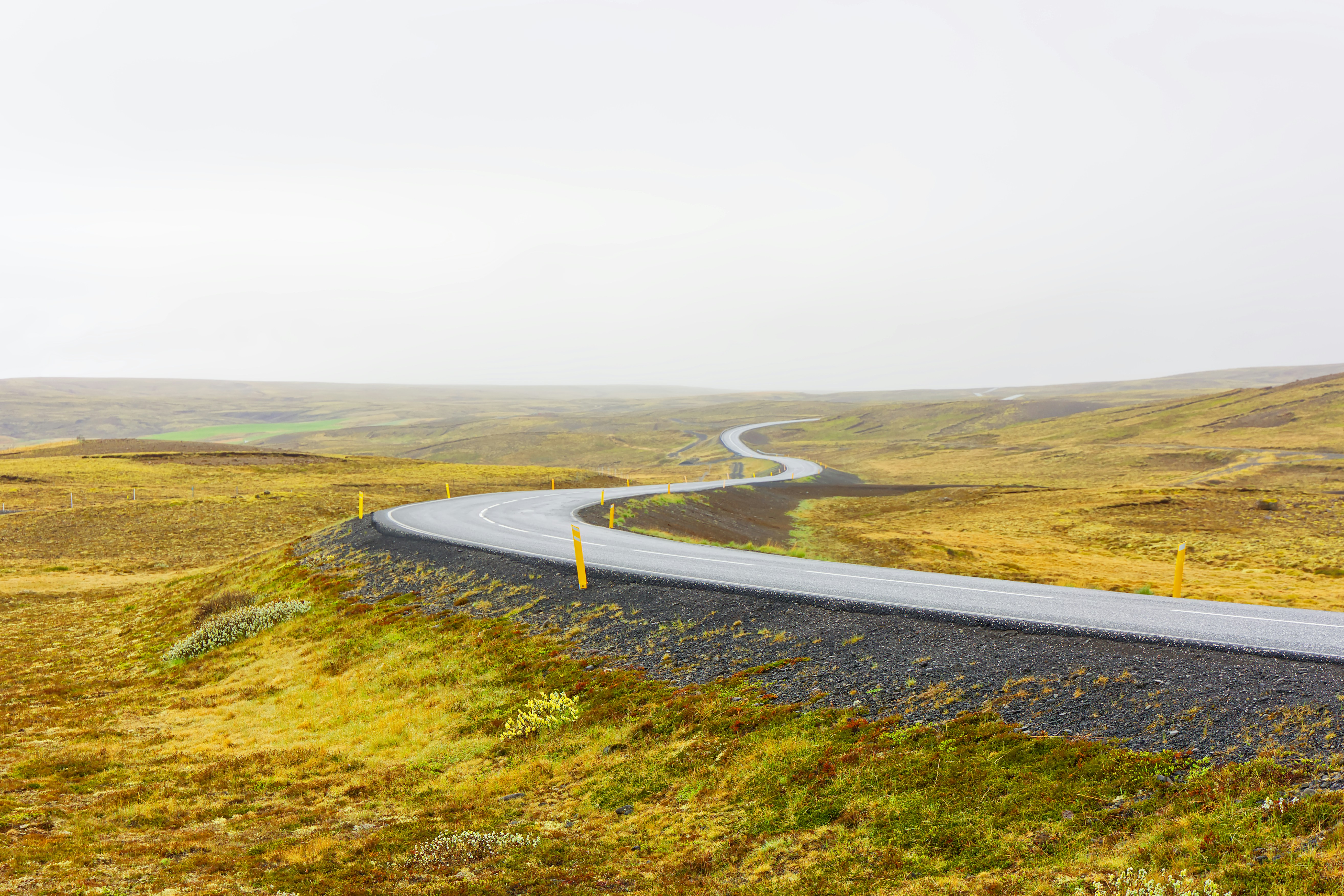 Winding asphalt road cutting through expansive moorland with muted autumn colors and low horizon.
