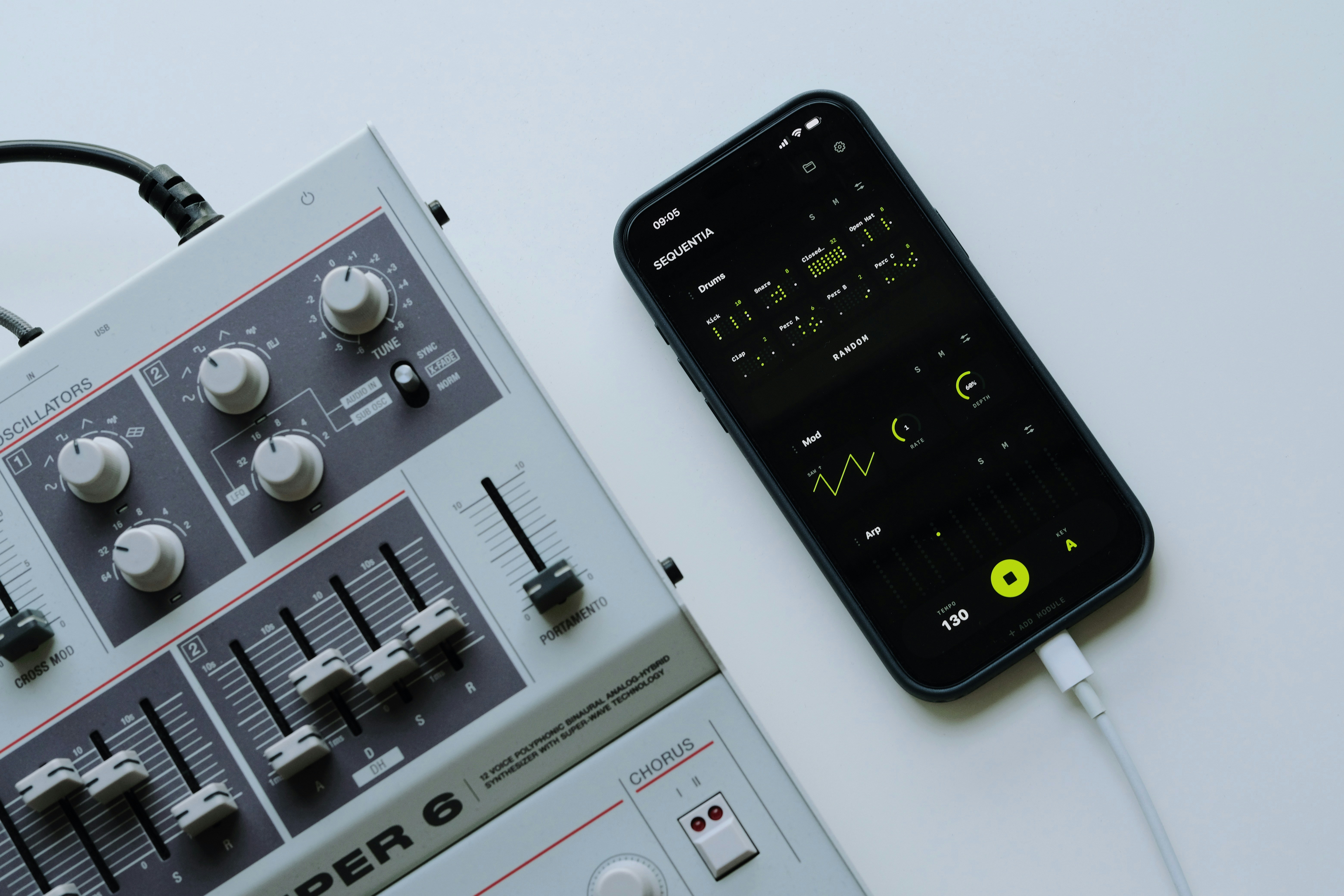 A close-up scene shows a vintage-styled audio mixer next to a smartphone connected via a charging cable, highlighting a modern device integrated with analog controls. The composition emphasizes contrast between tactile knobs and a digital screen.