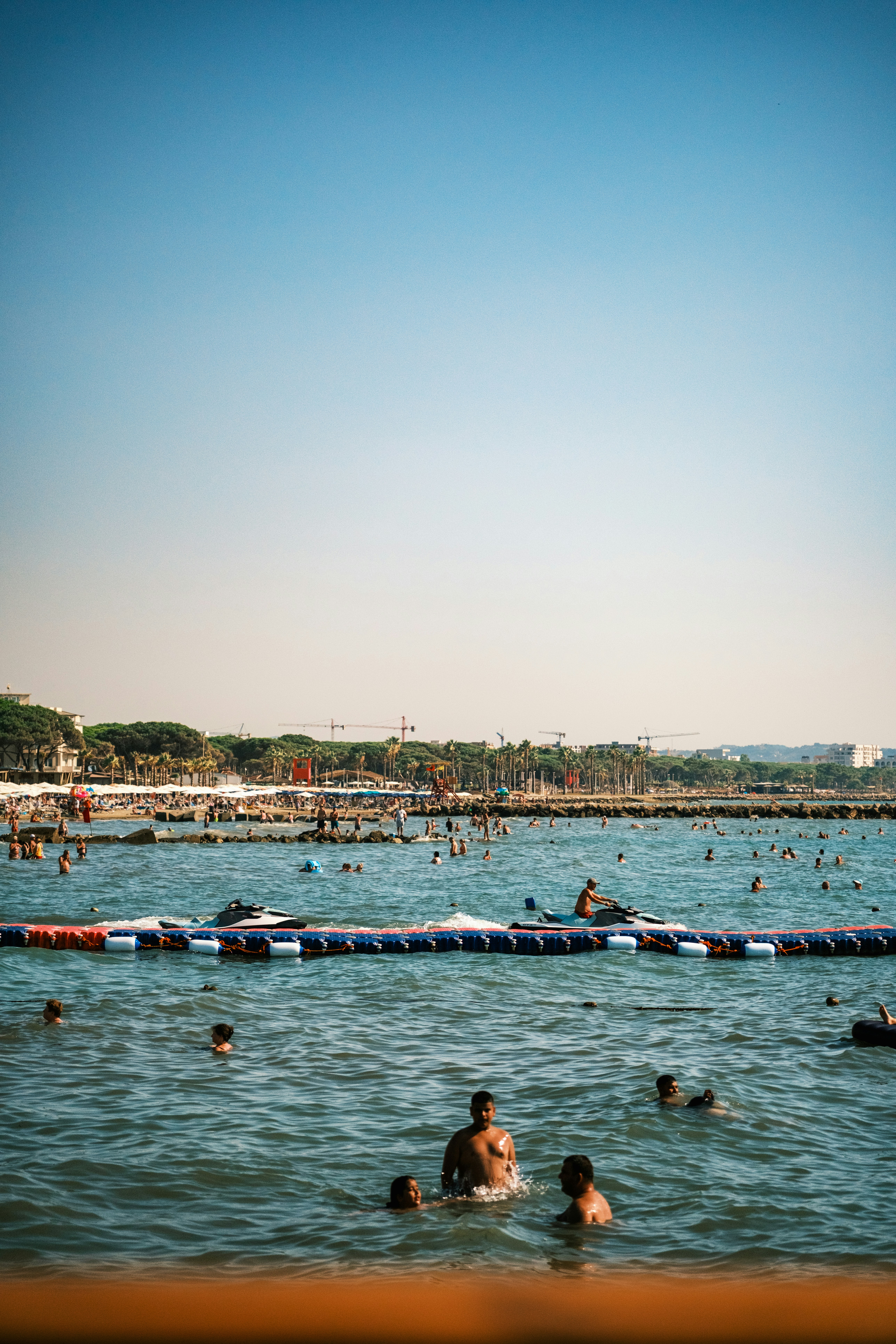 Sunlit Beachscape: People and calm waves along a busy shoreline