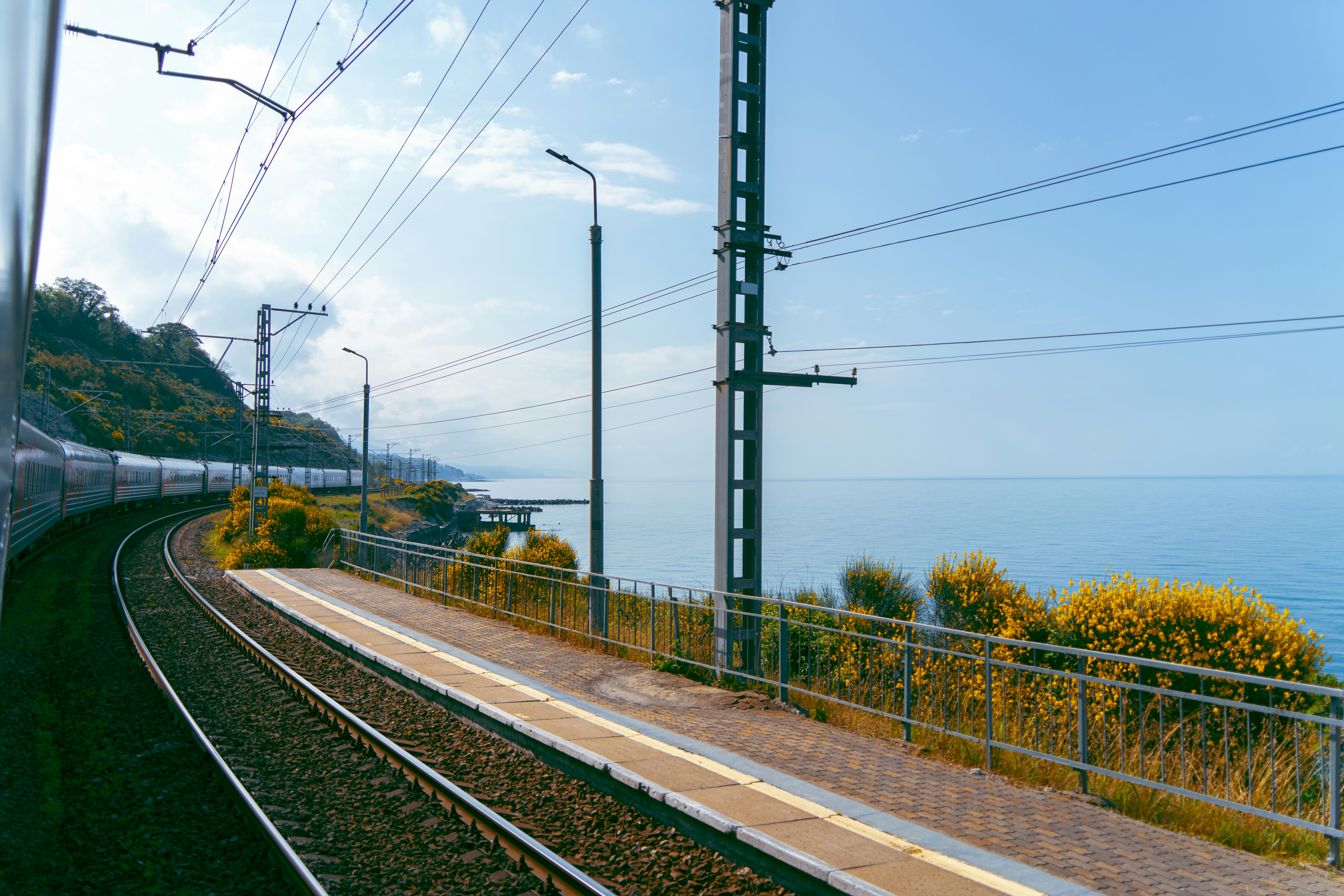 Railway tracks, platform, and ocean under a clear sky.
