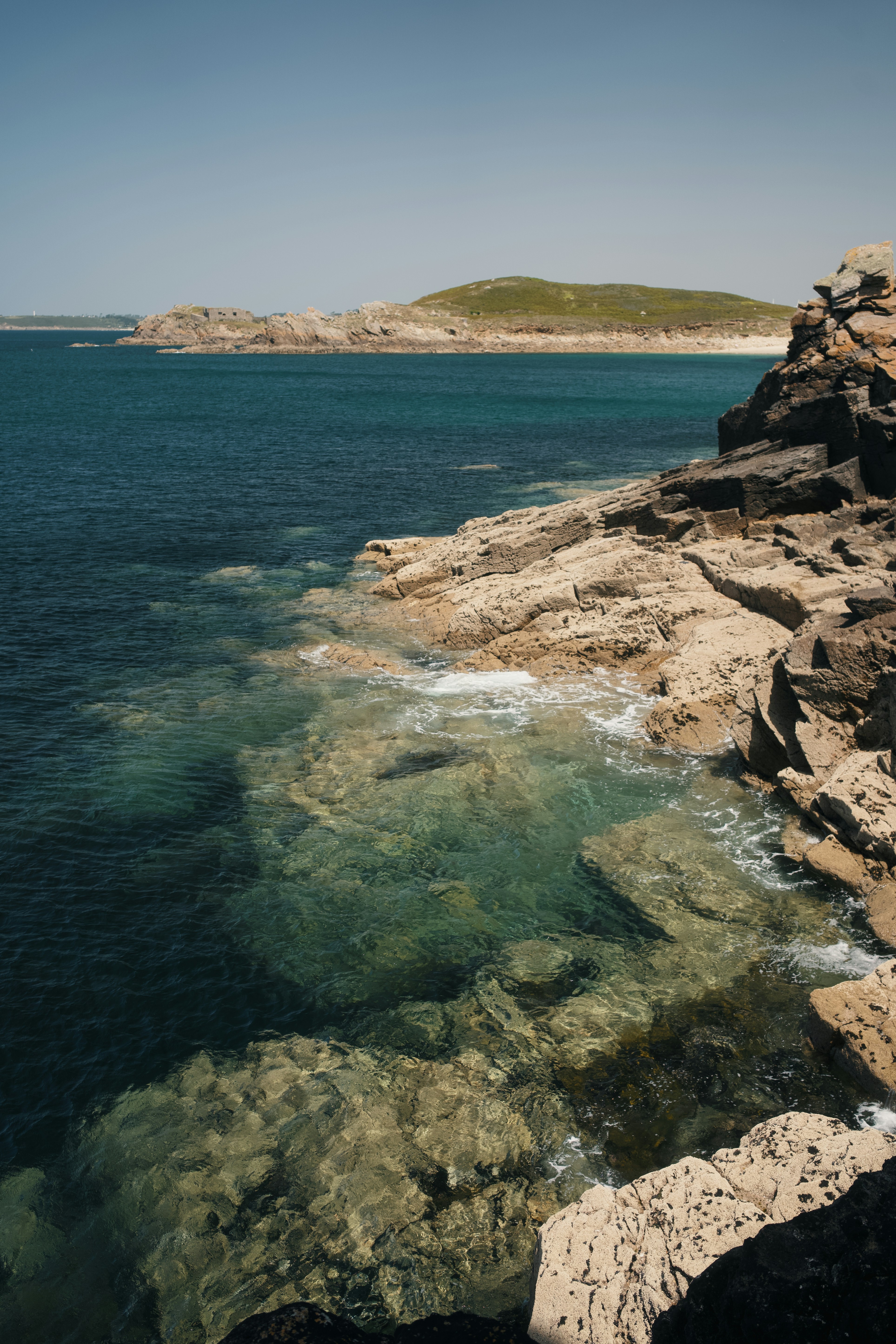Rugged Coastal Light: Sunlit Rockscape Over Calm Turquoise Waters