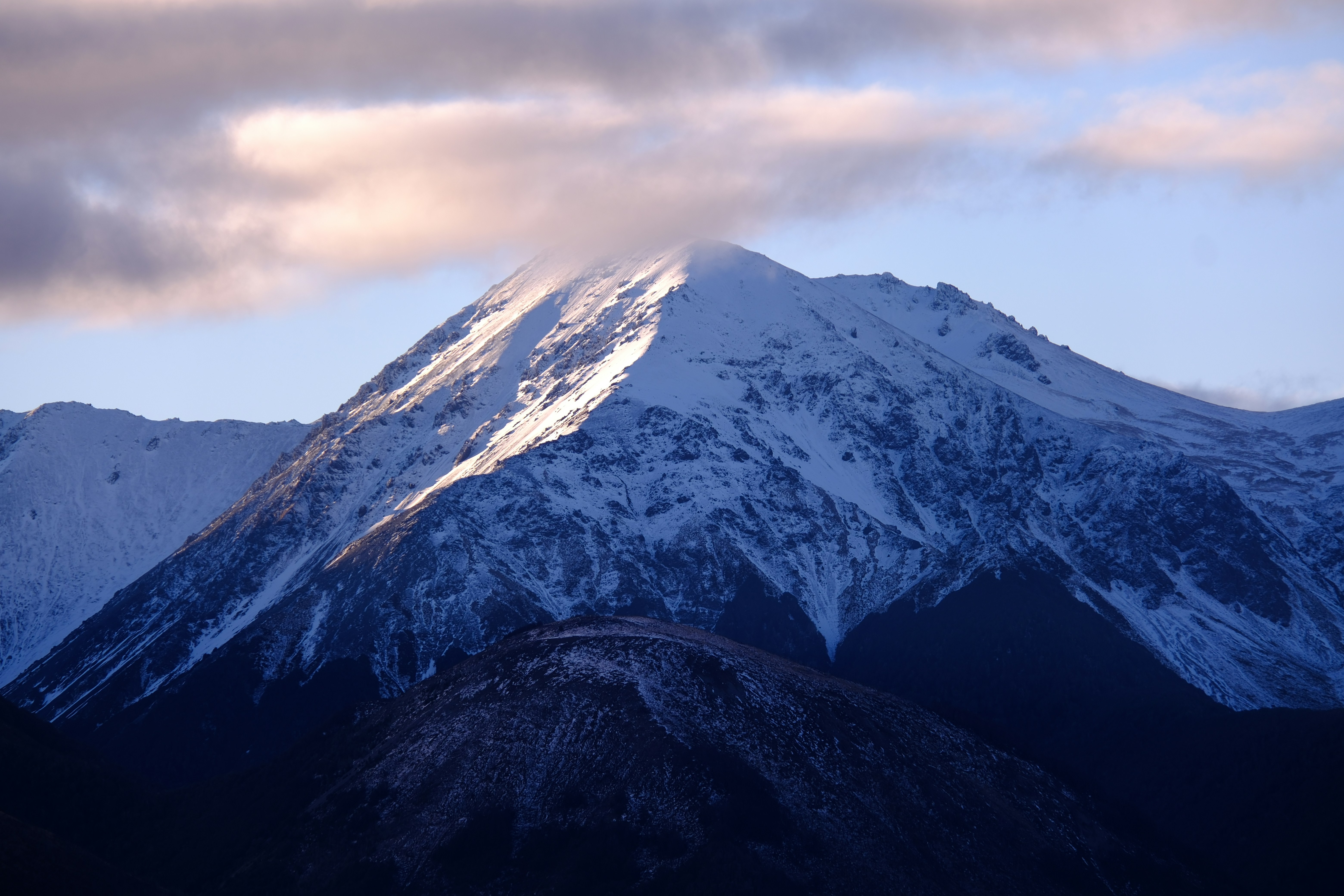 Sunlit Peak Crowned by Clouds Over Distant Range