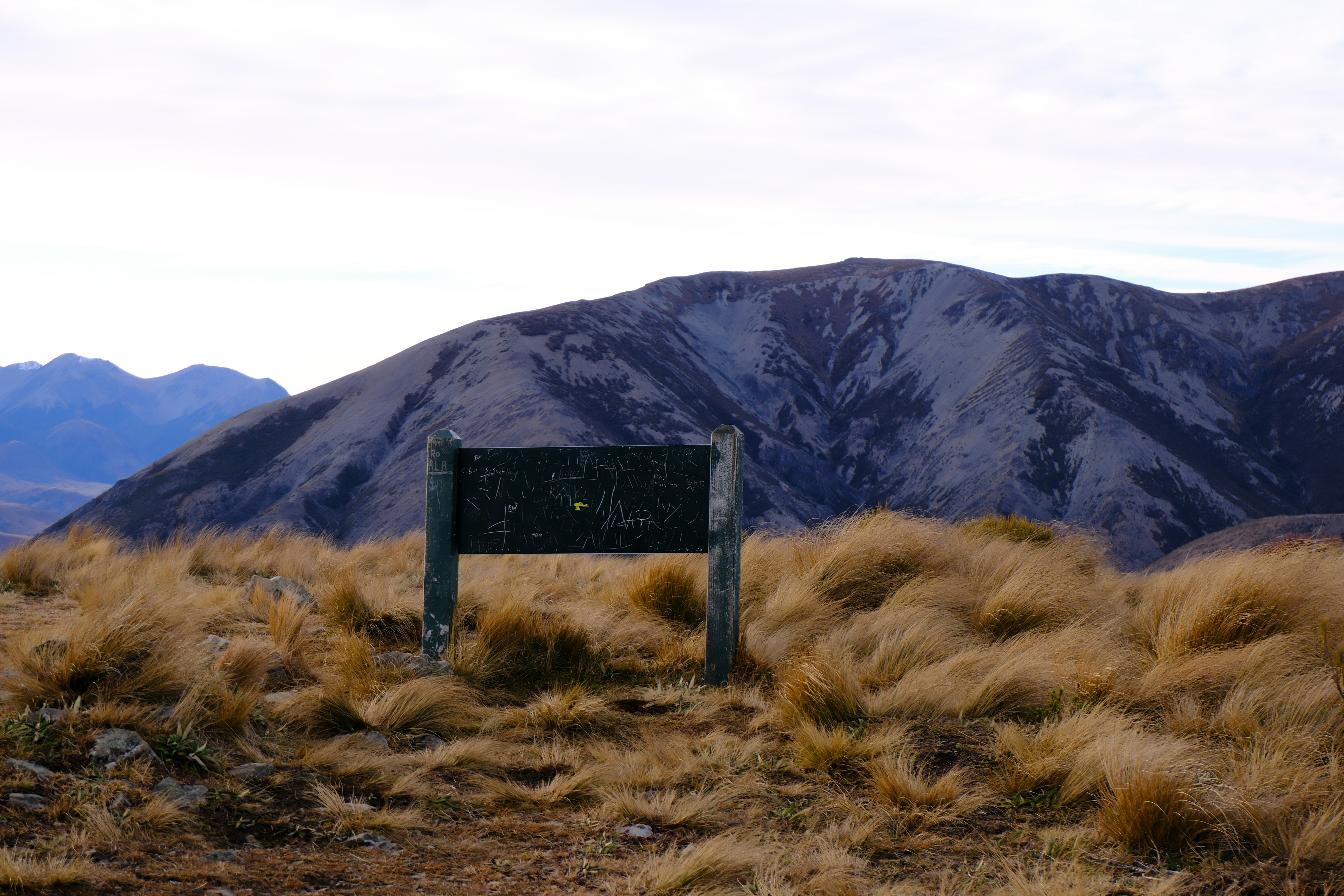 Deserted summit sign standing guard over windswept grass and distant ridge
