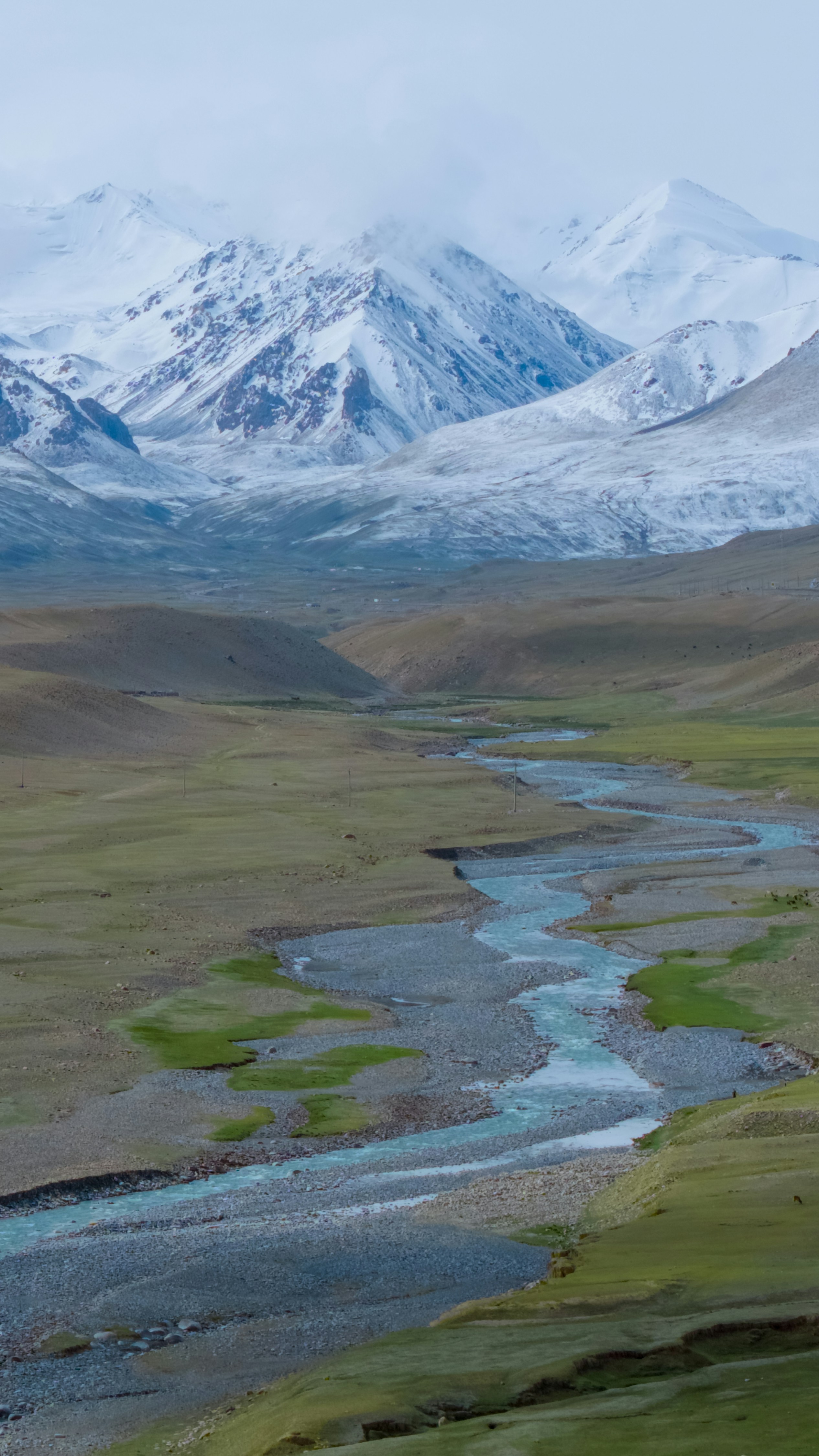 Glacial Stream Winding Through Alpine Valleys Beneath Snow-Crowned Peaks