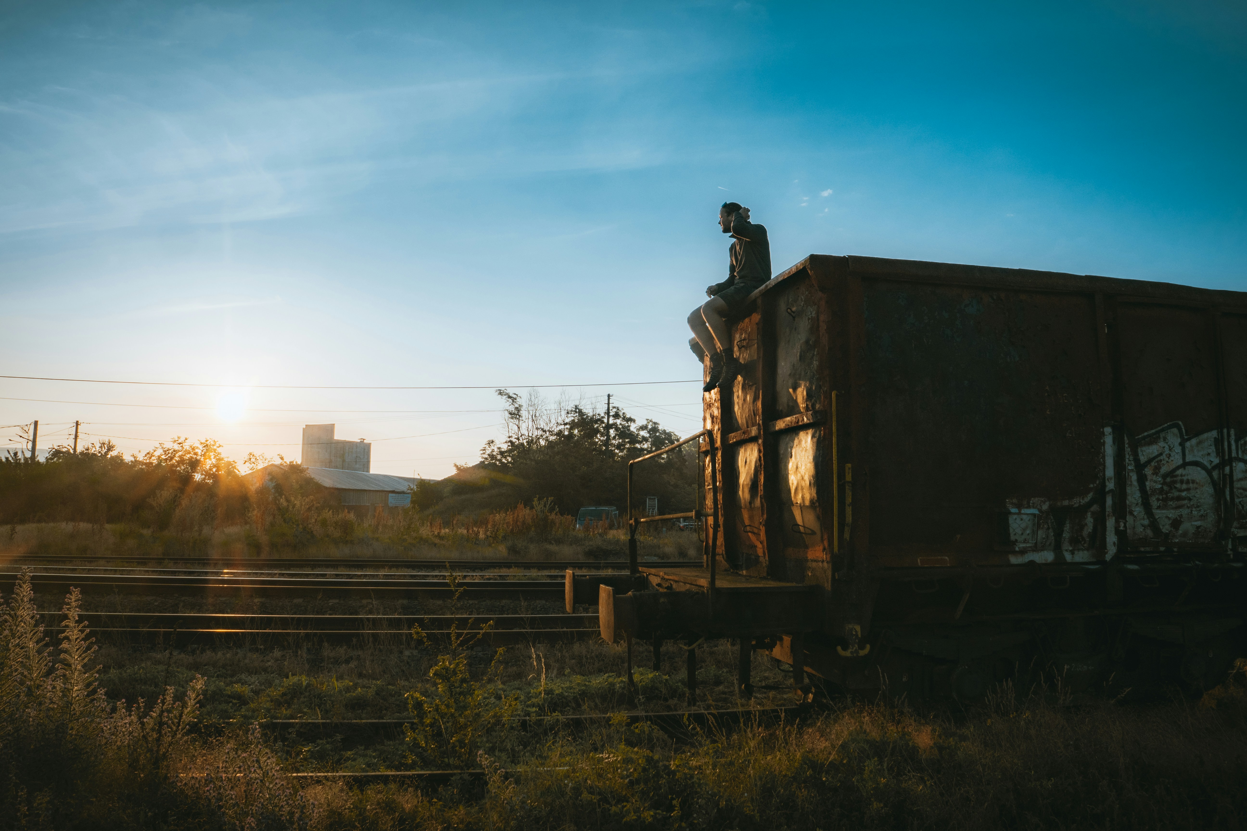 Person sitting on a train car at sunset near tracks.