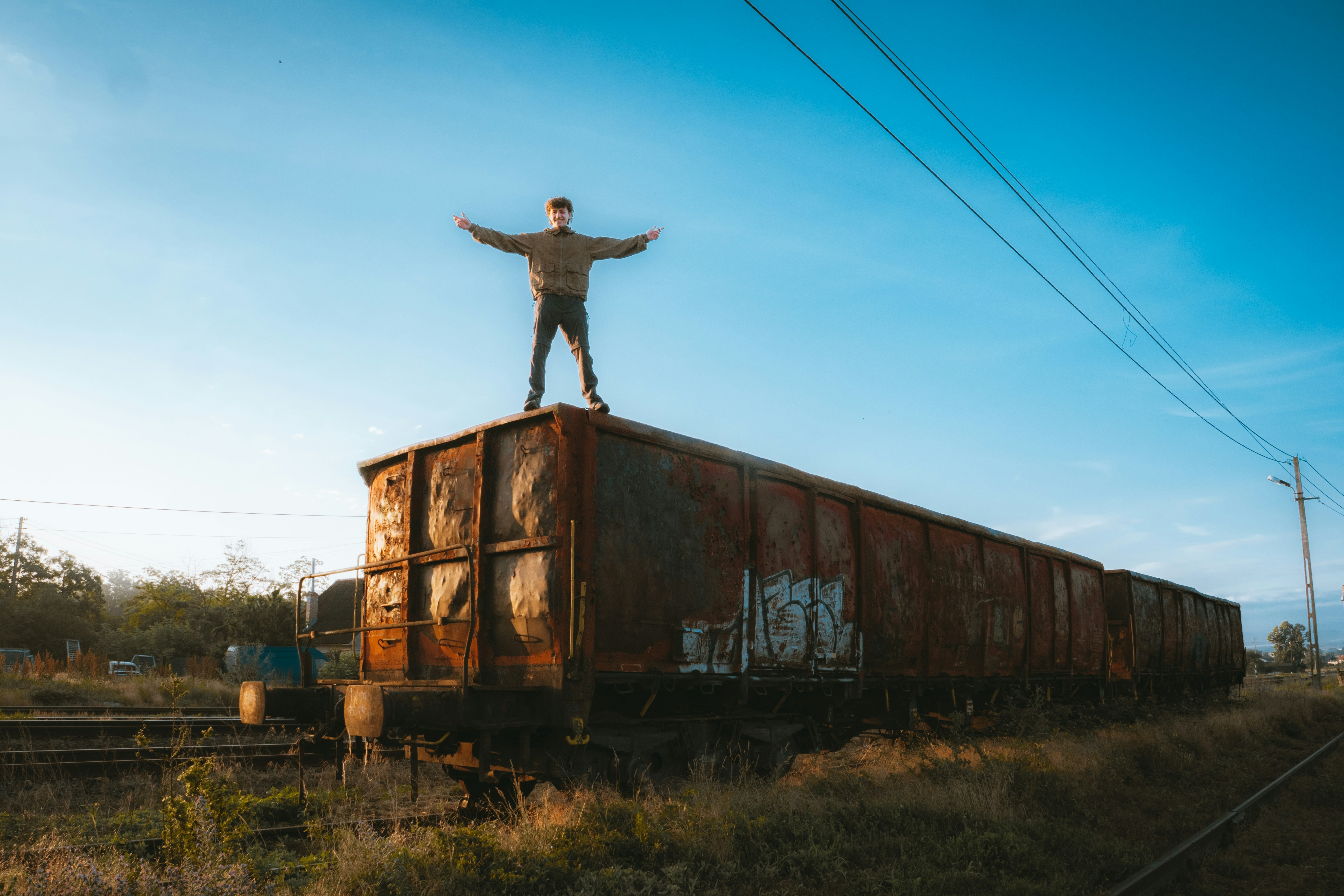Man with arms Raised atop a rusted freight car under a clear blue sky