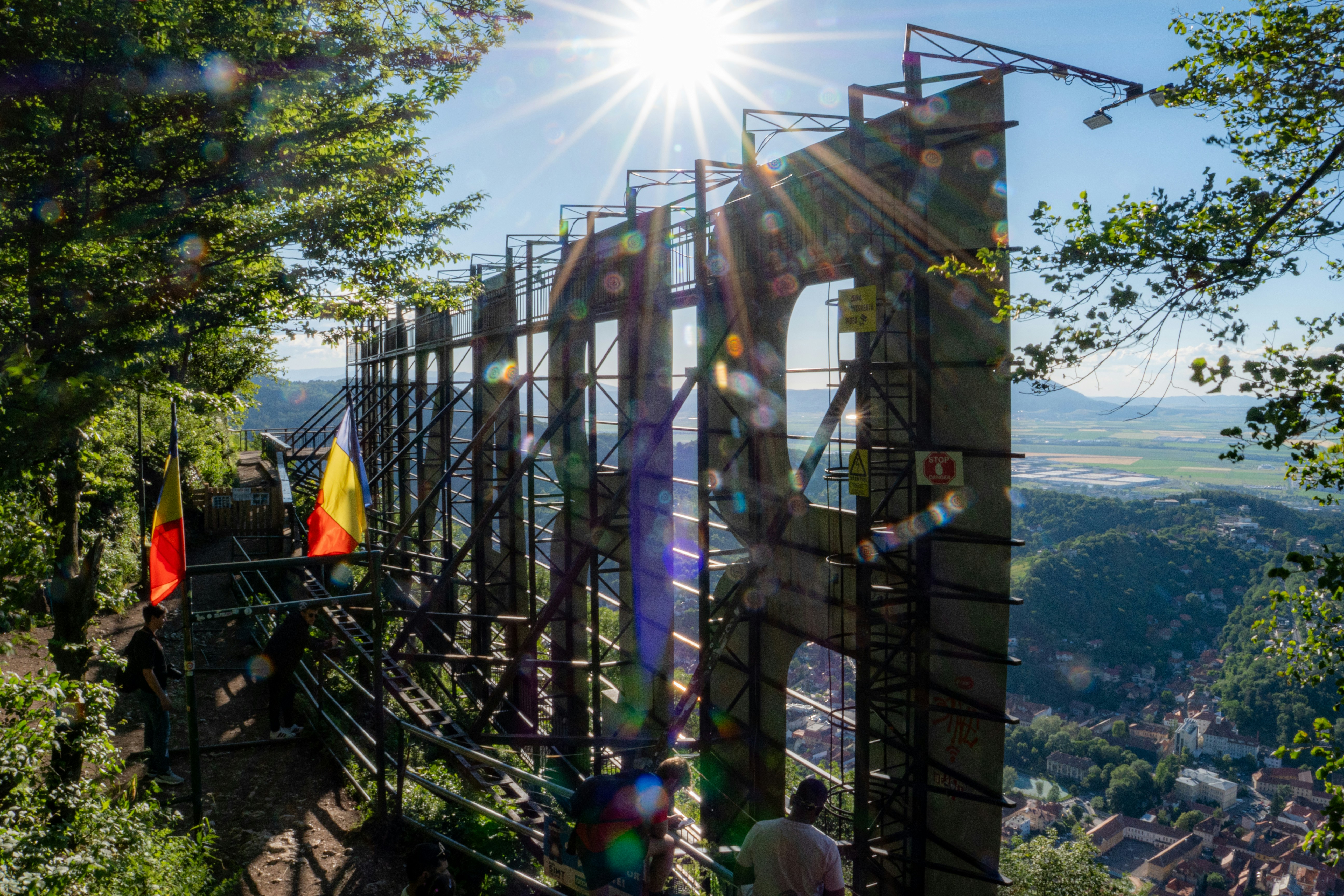 Sunlit Framework: A hillside stage of steel and flags against a panoramic valley