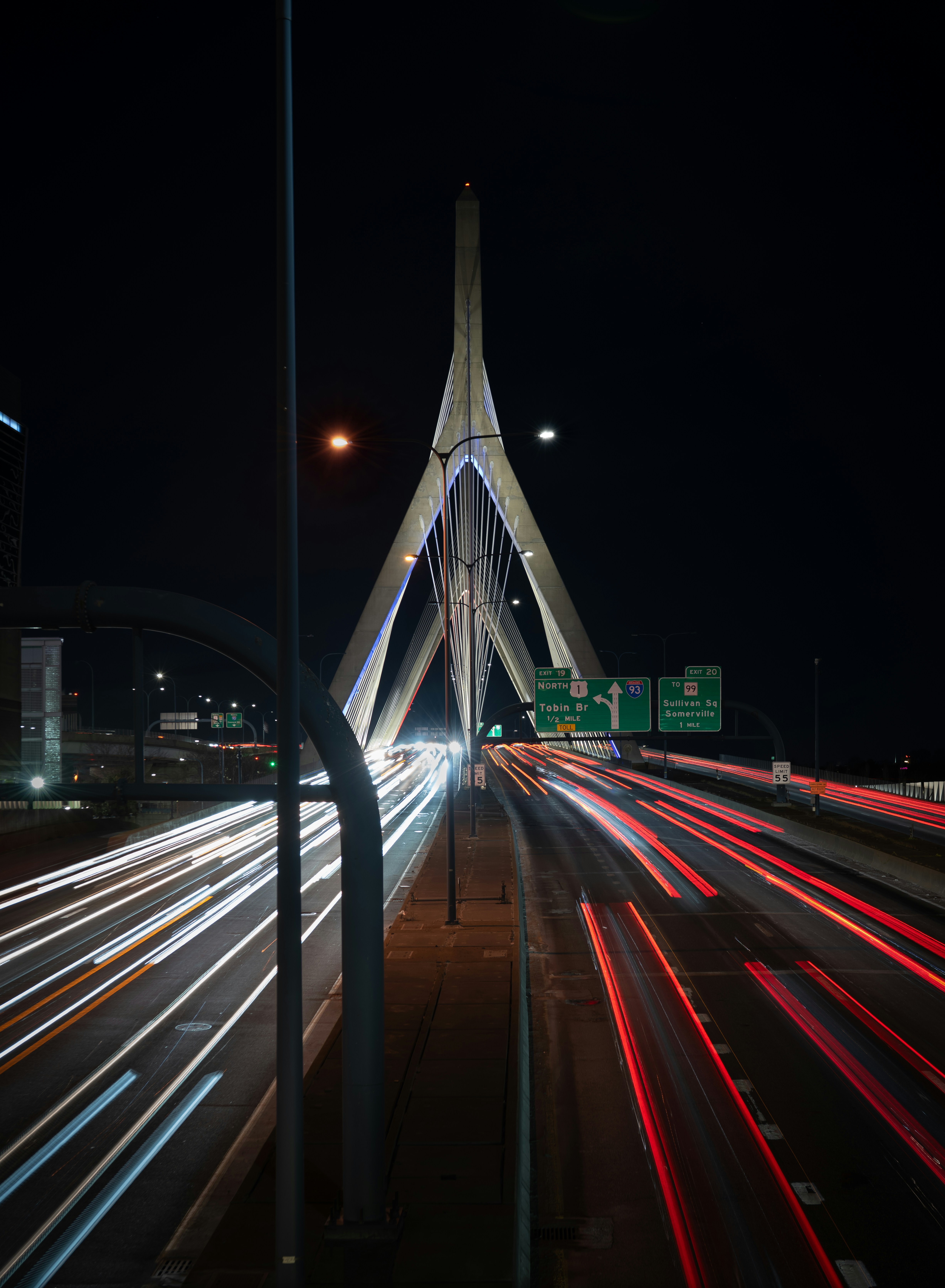 Cable-stayed dawn: a lone tower and tear-shaped arch pierce the night as light trails collide on a neon highway