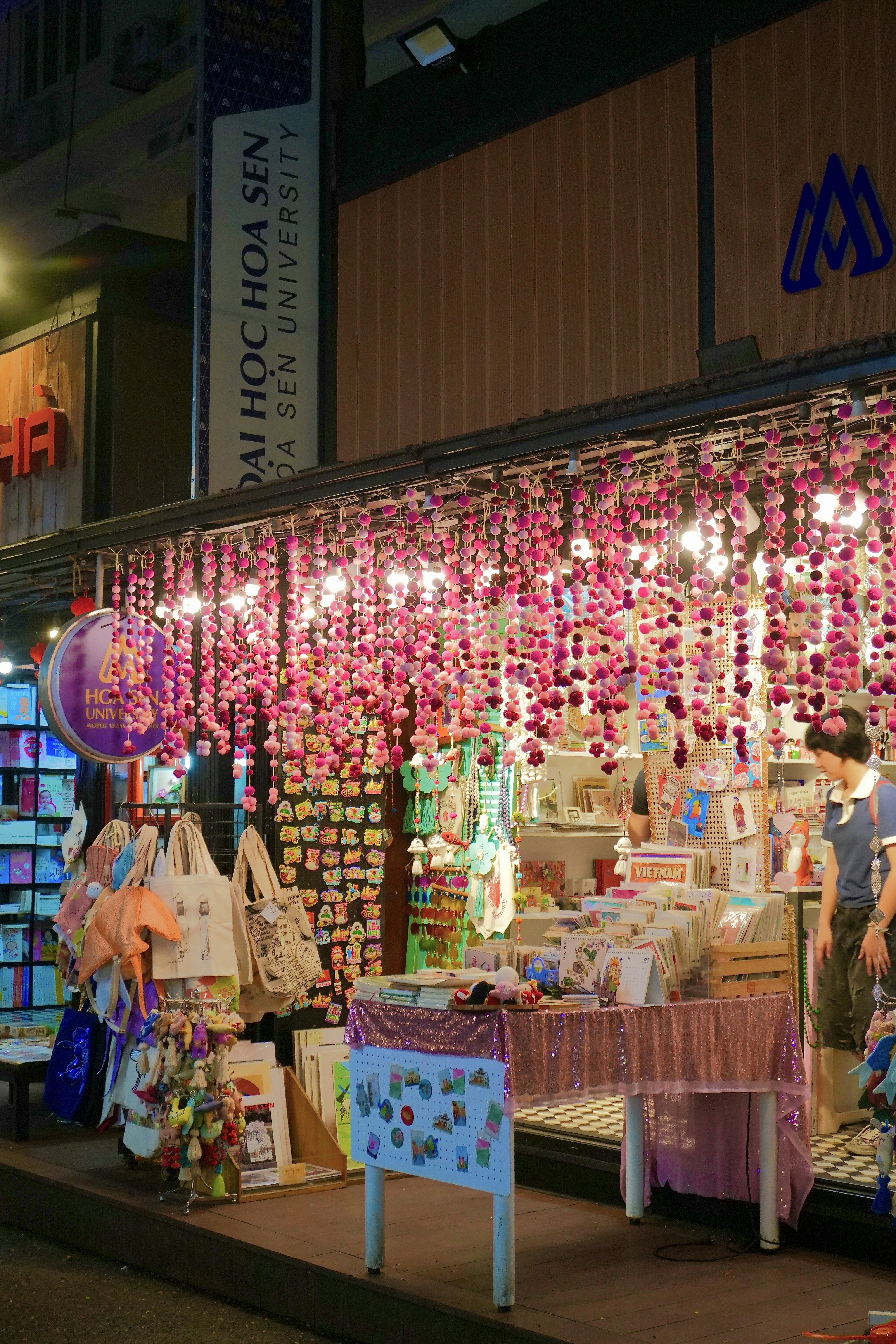 Vibrant storefront with hanging bead decor and a street market stall filled with colorful souvenirs and a worker arranging items.